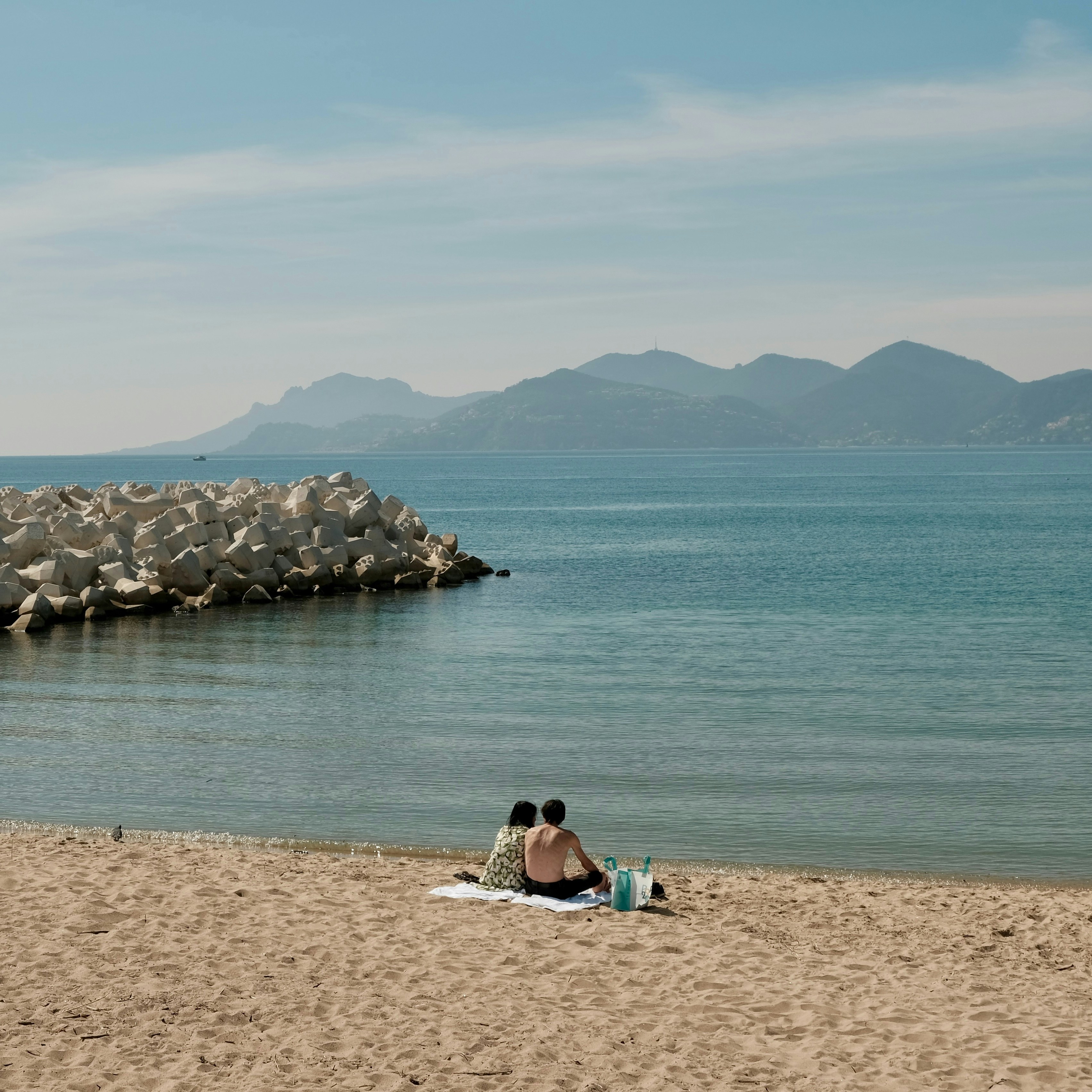 Quiet Couple by the Breakwater: A Seaside Moment Framed by Distant Peaks