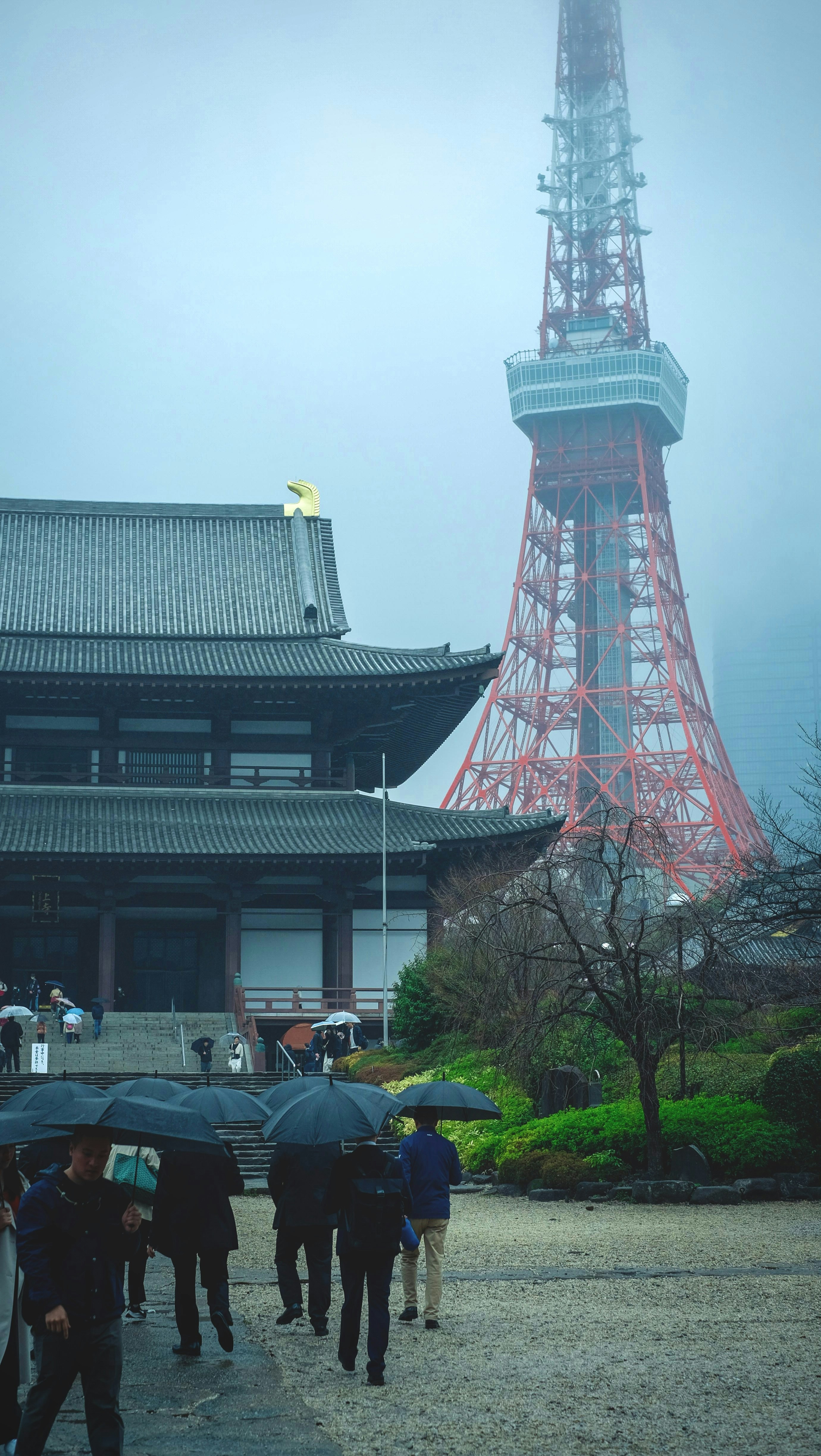 Tokyo tower foggy day | a group of people holding umbrellas in front of a building