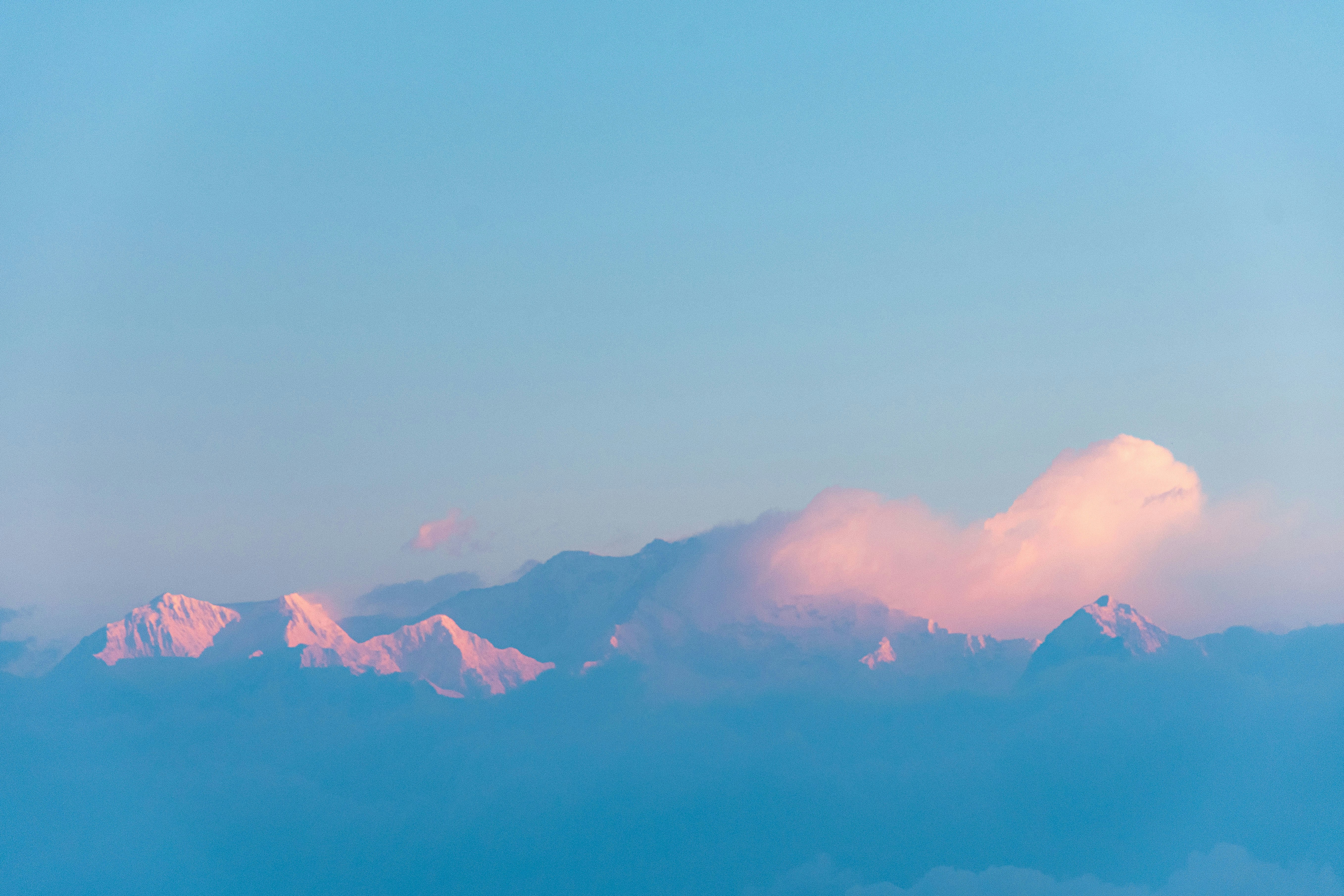 Soft pastel hues illuminate the rugged silhouettes of Himalayan mountains, with wispy clouds drifting above. A serene moment captured in the early light.