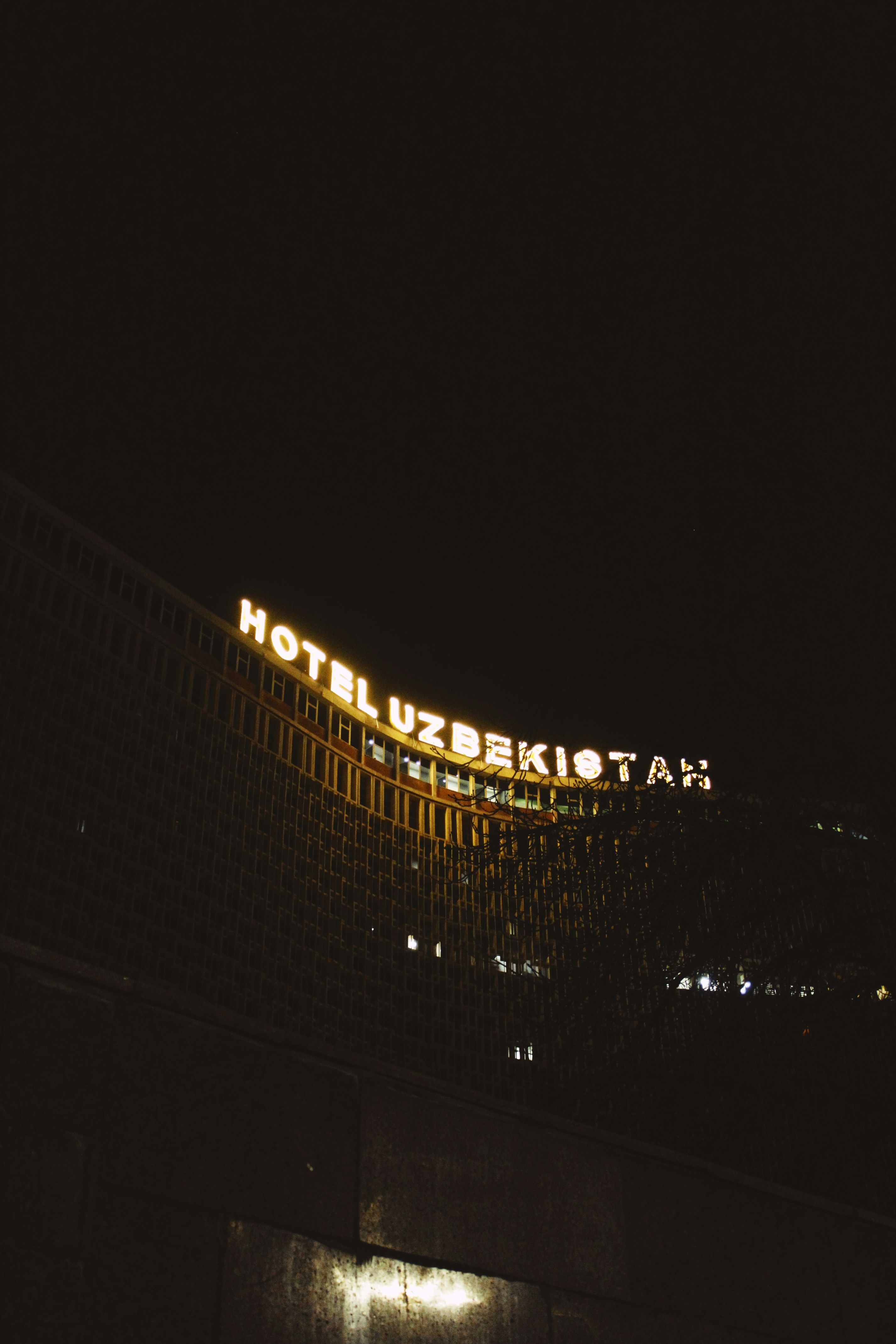 Neon sign of Hotel Luzbekistan glowing against a dark night sky, showcasing modern architecture and inviting ambiance.