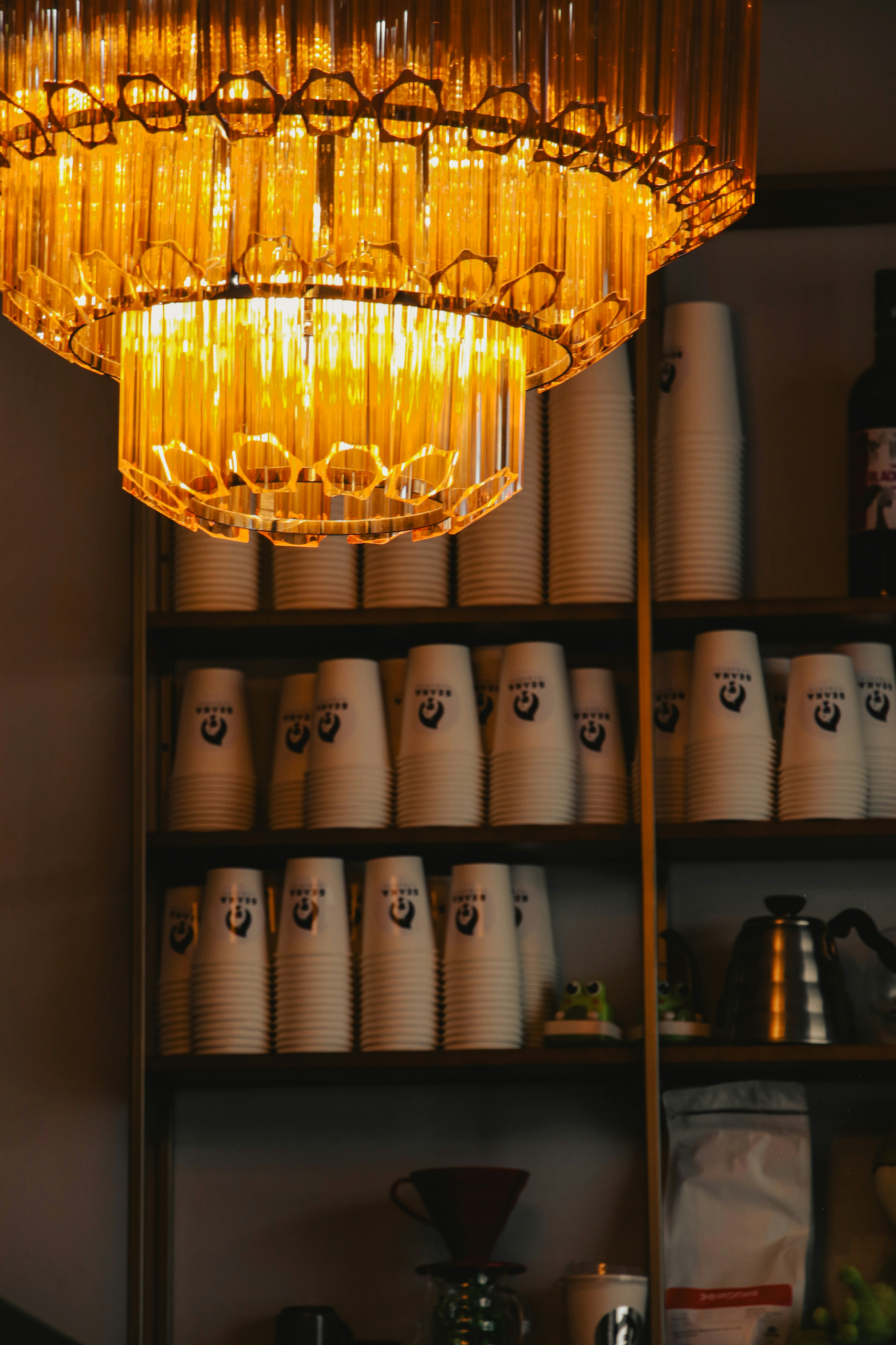 Amber Chandelier Over the Cup Wall: A Quiet Café Moment