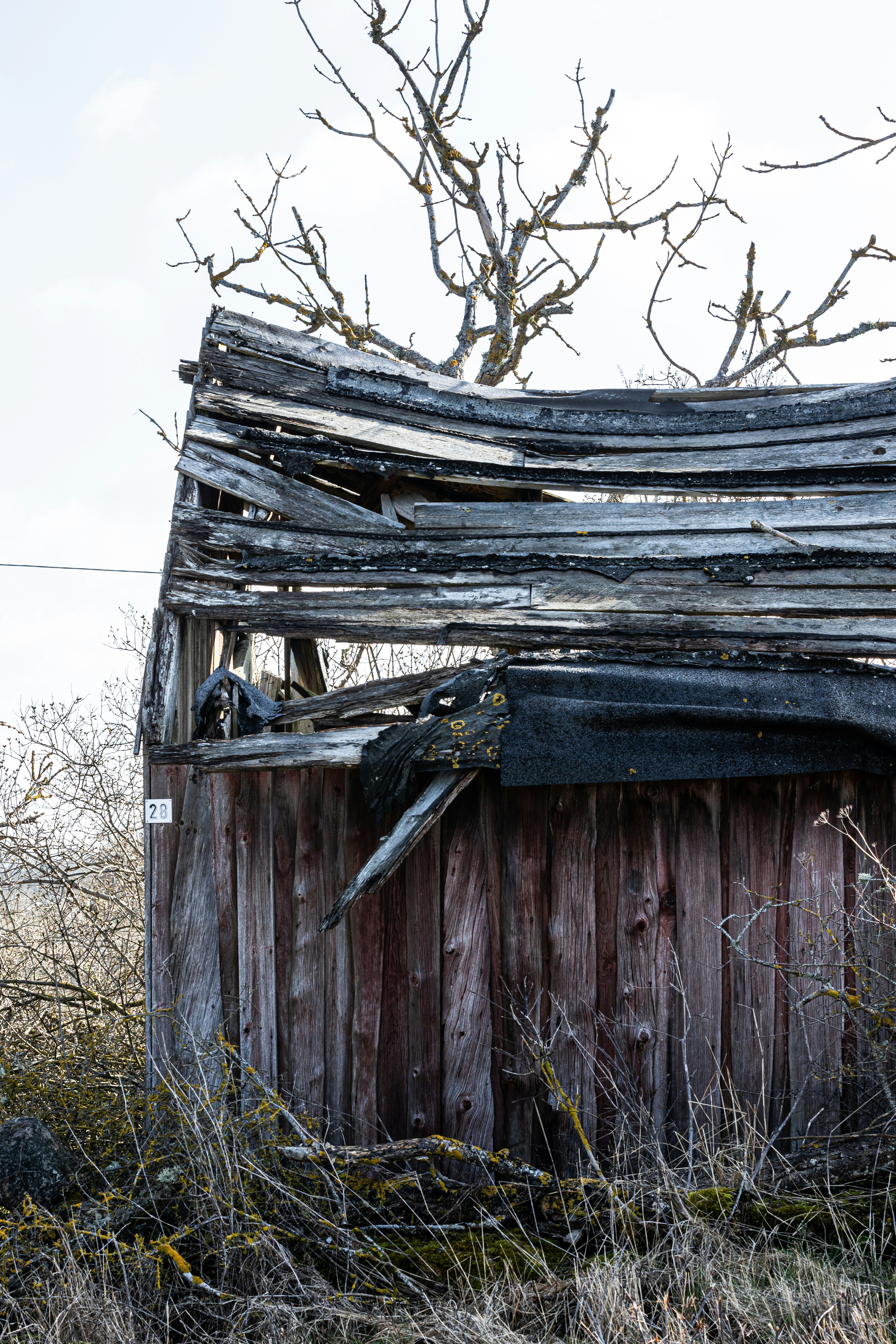 A derelict building in the countryside | an old wooden shed with a broken roof