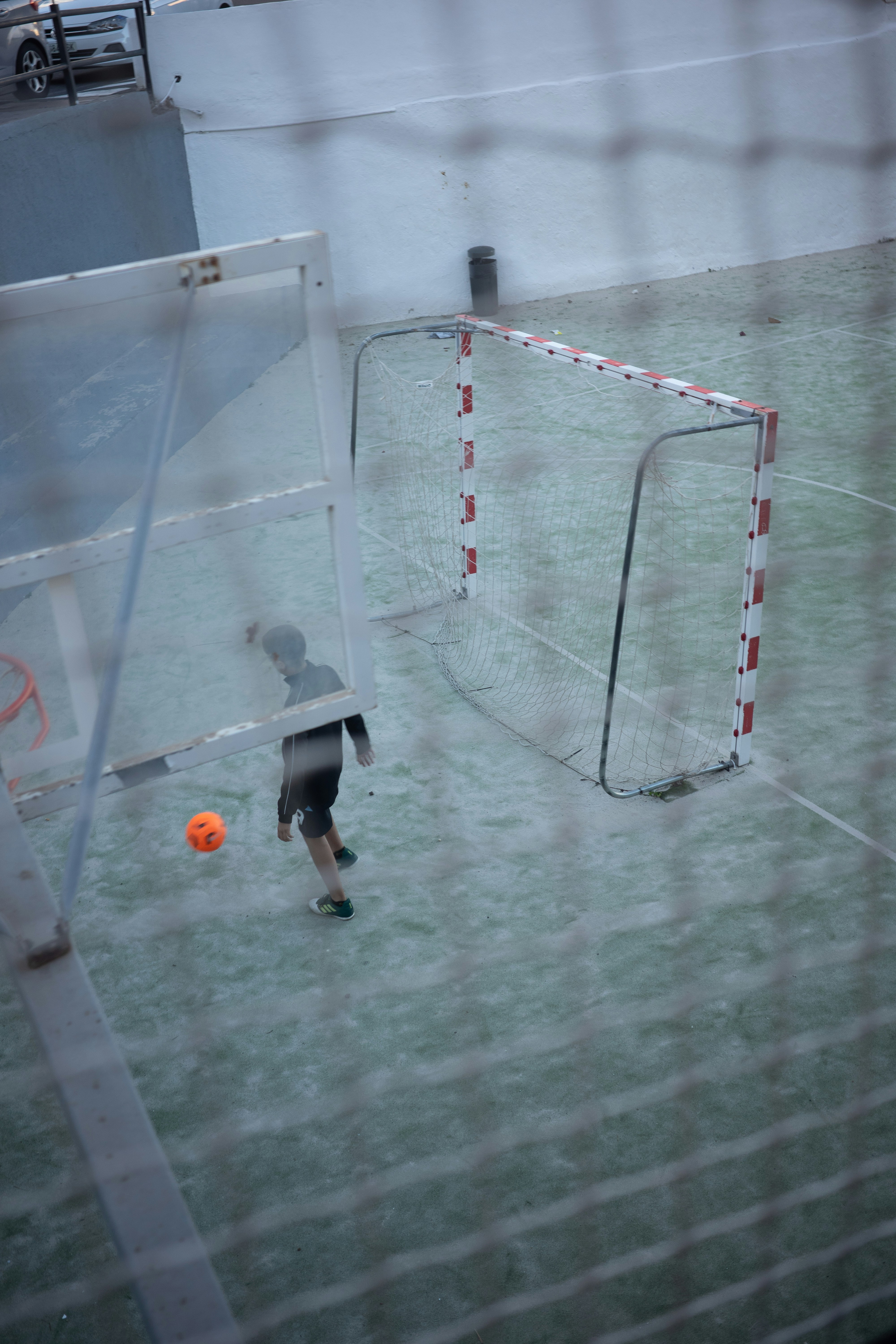 Rooftop Futsal: Orange Ball Dribble Beyond Glass and Net