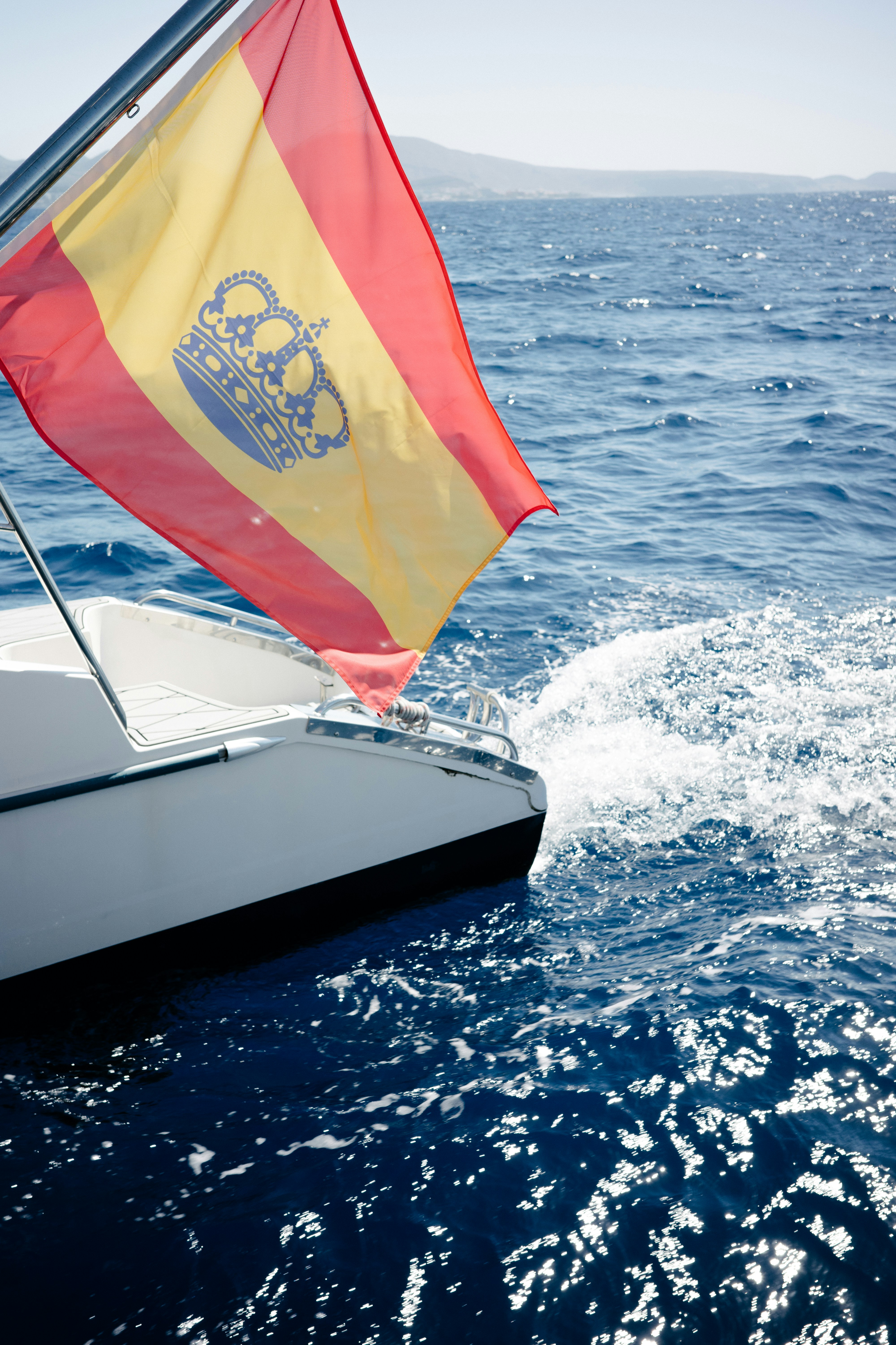 Flag Against Sapphire Wake: Spain on a Sunlit Sea