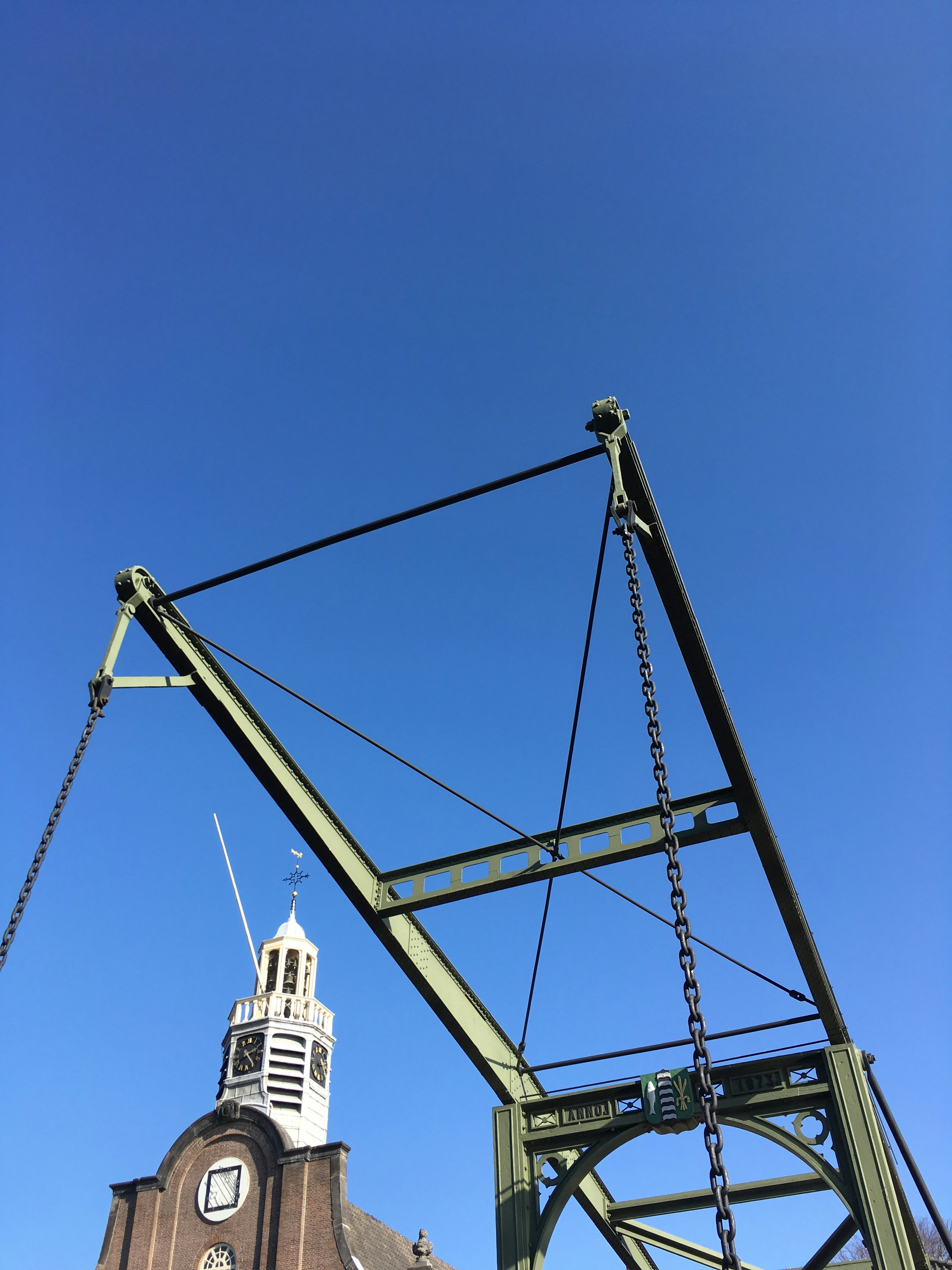 Crisscross Horizon: Green Iron Frame Framing a Clock Tower Against a Cerulean Sky
