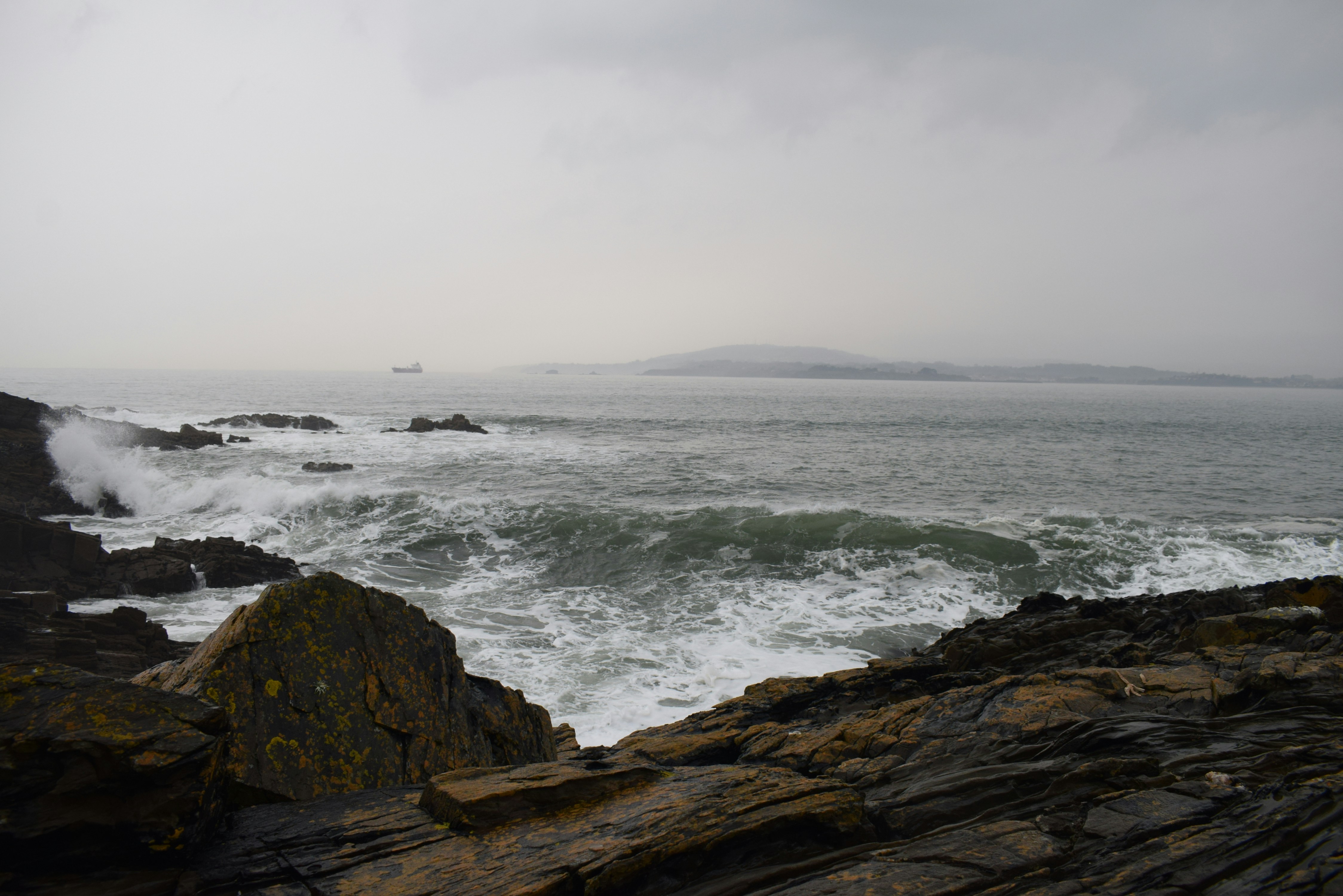 Waves crashing against rocky shore under a cloudy sky.