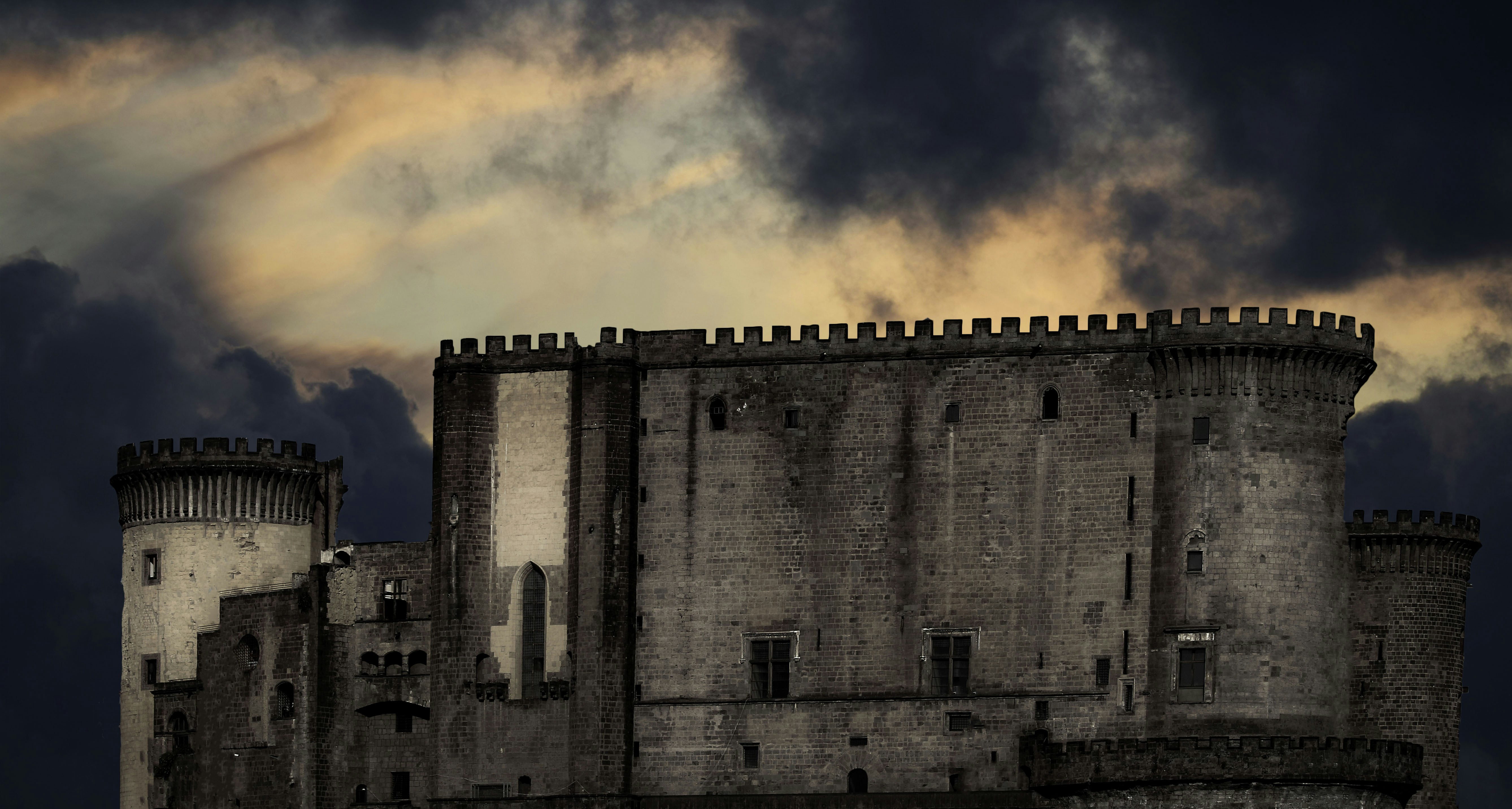 Ancient stone fortress silhouetted against dramatic, cloud-filled sky at dusk.
