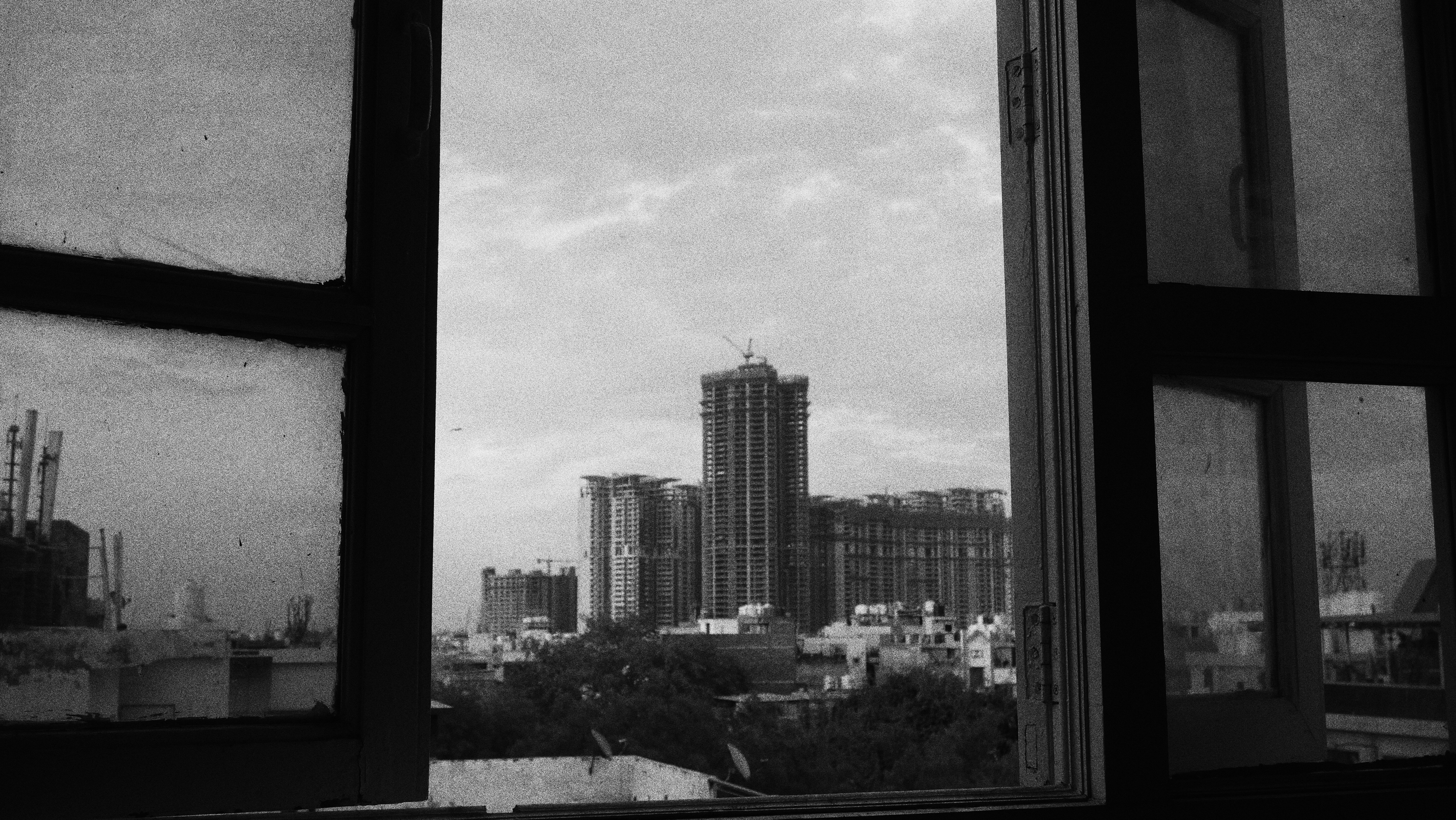 Monochrome urban skyline viewed through window panes, with a central skyscraper dominating the mid-ground. The composition uses the window frames to create depth and framing.