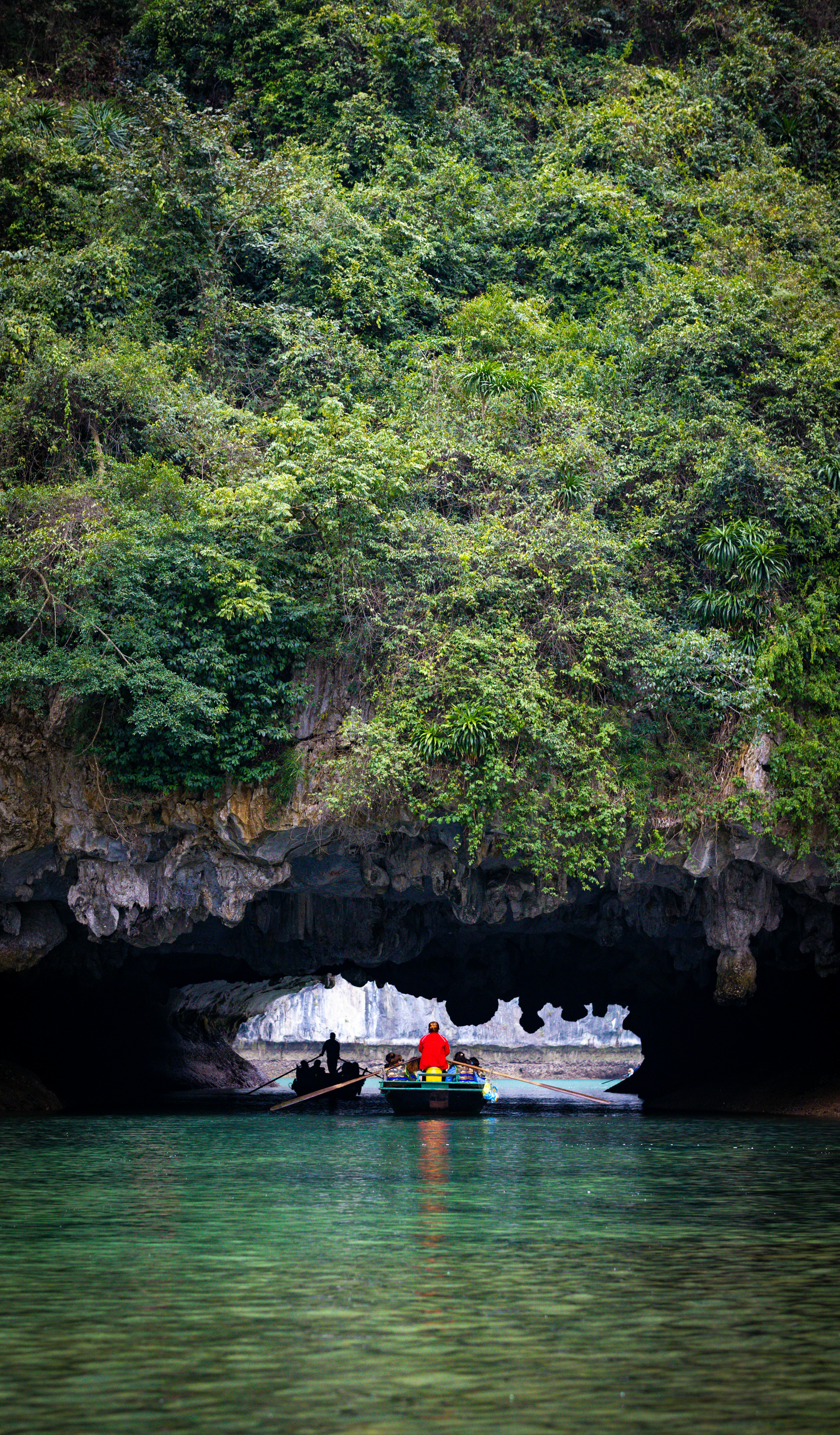 Emerald Archway: Boat Glides Through a Jungle-Crowned Sea Cave