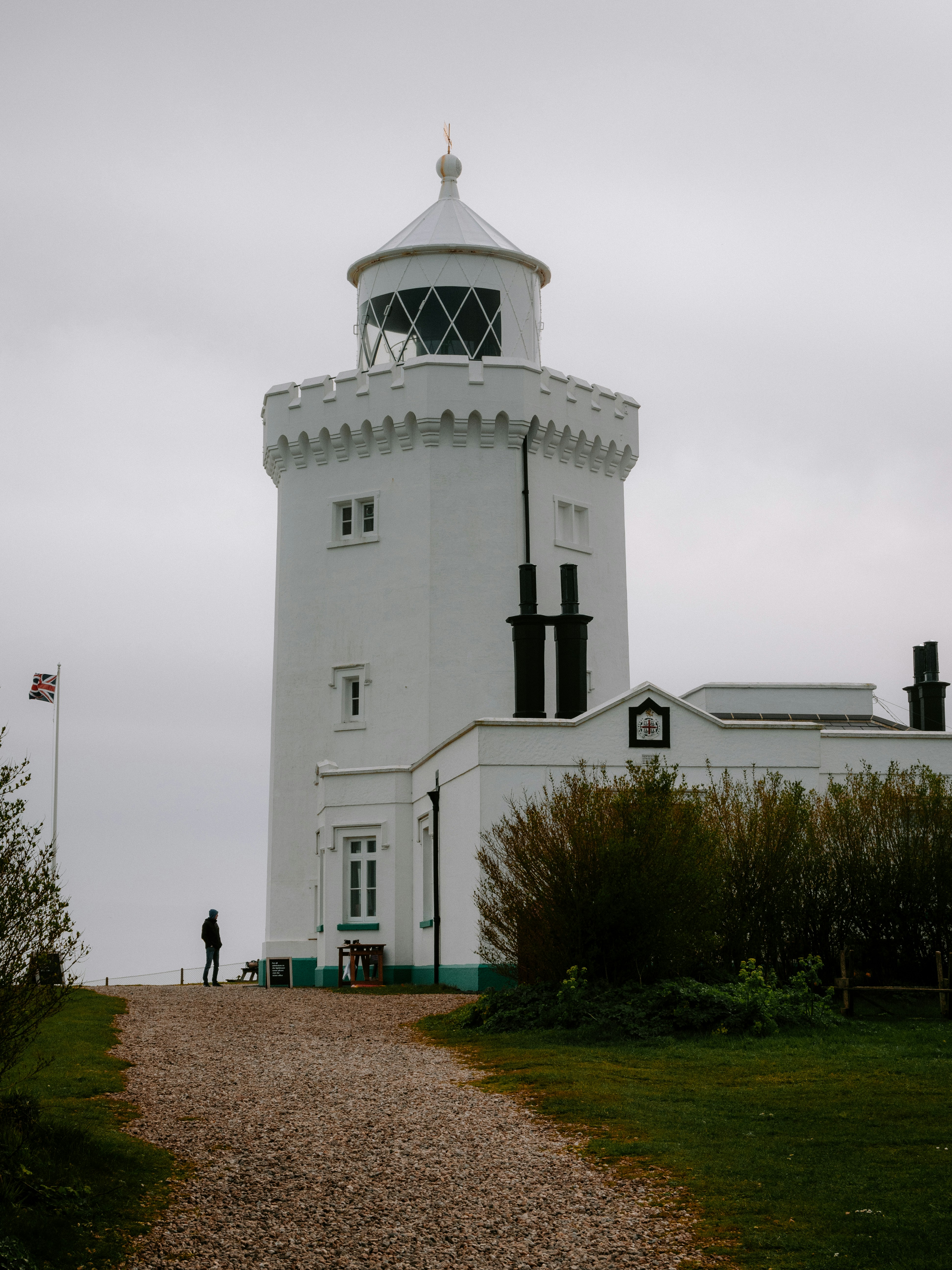 White Sentinel by the Pebble Path: A Quiet Lighthouse Under an Overcast Sky