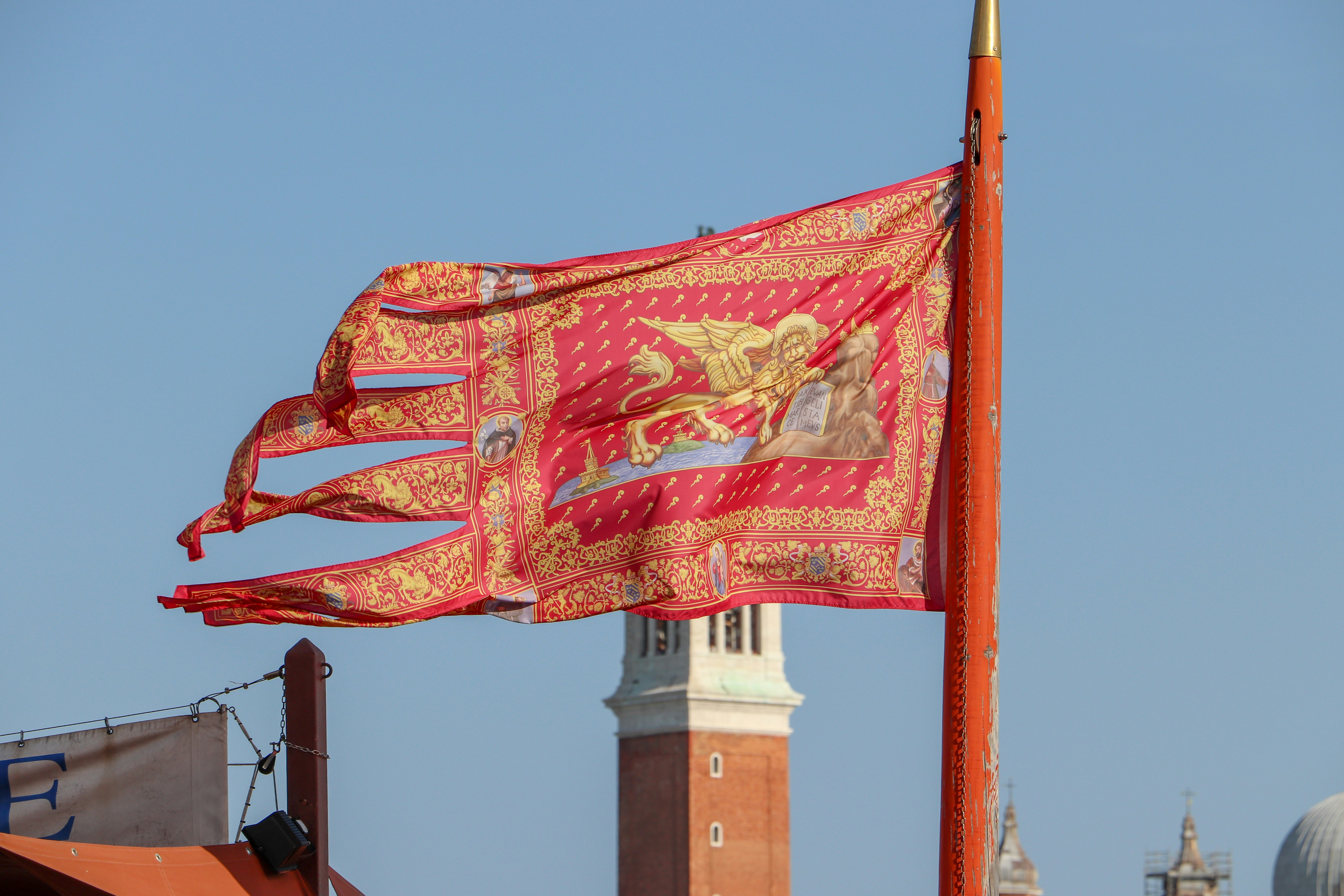 A red and gold flag with a clock tower in the background photo – Free ...
