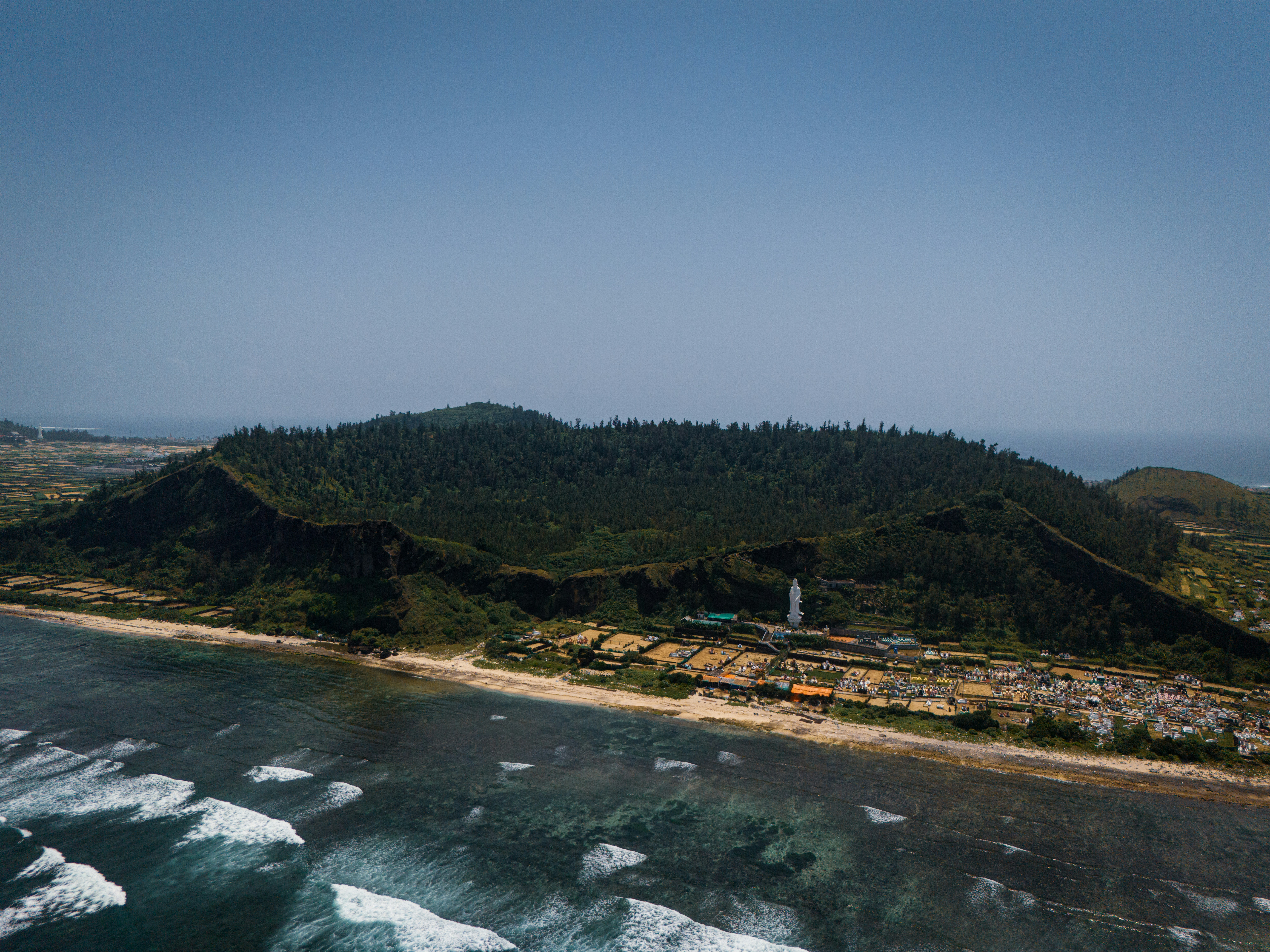 A lighthouse perched atop a lush, green island surrounded by azure ocean waves under a clear sky.