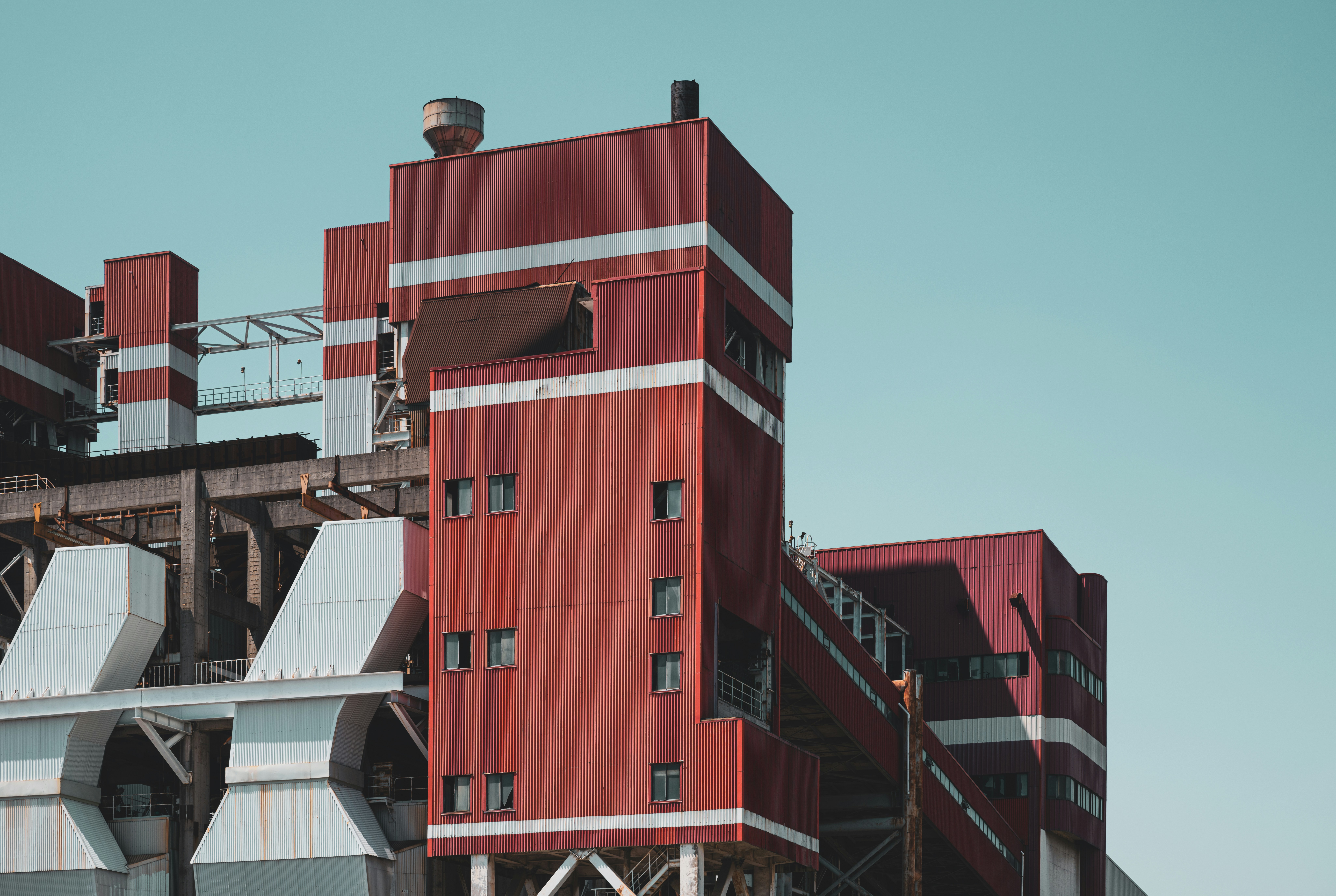 A striking red industrial building showcasing modern architecture and intricate structural design against a clear blue sky.