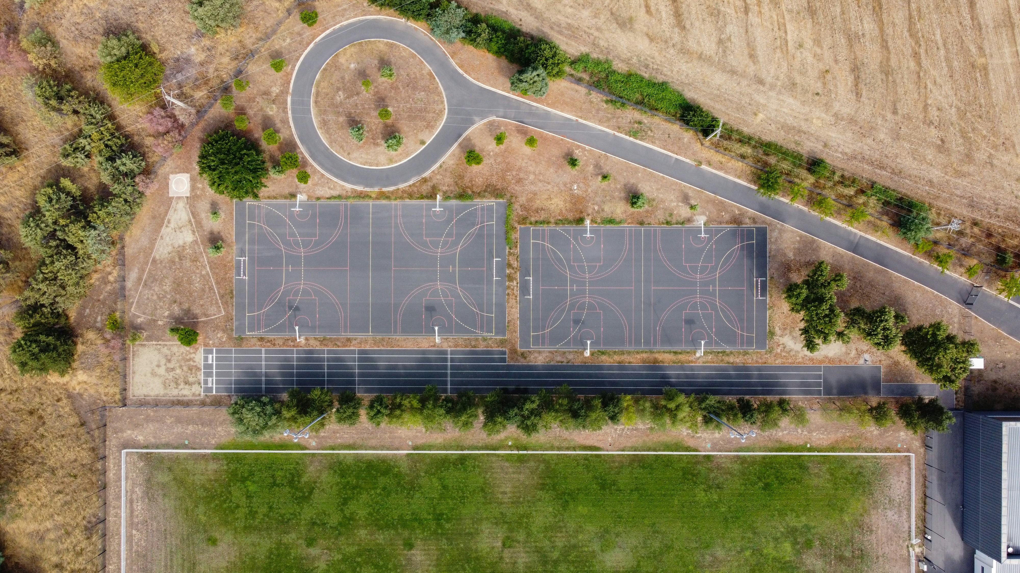 Aerial view of basketball courts and pathways surrounded by greenery, showcasing organized sports facilities in an urban setting.