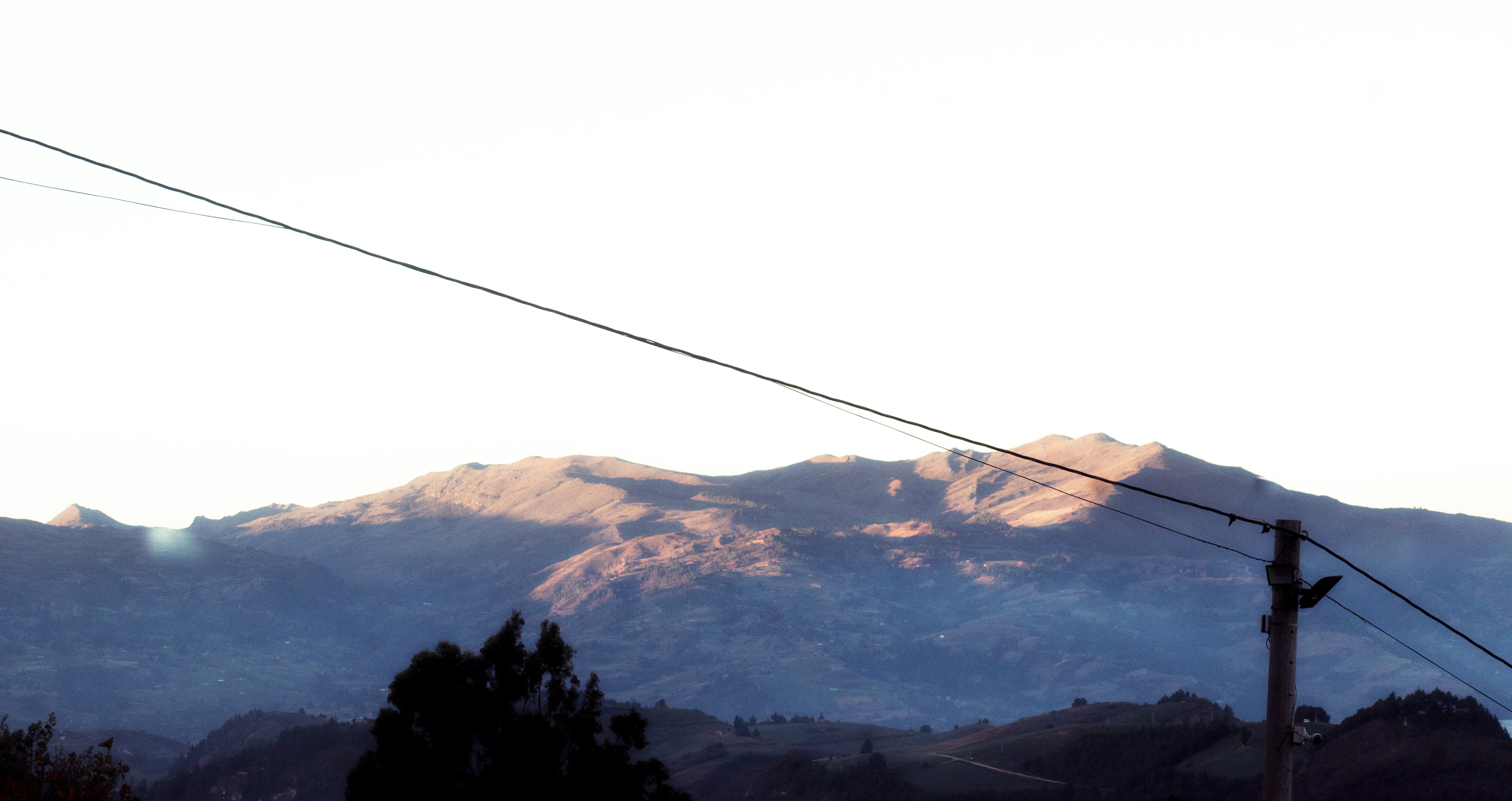 Sunlit mountain range with power lines crossing the foreground, highlighting the intersection of natural and human-made landscapes.