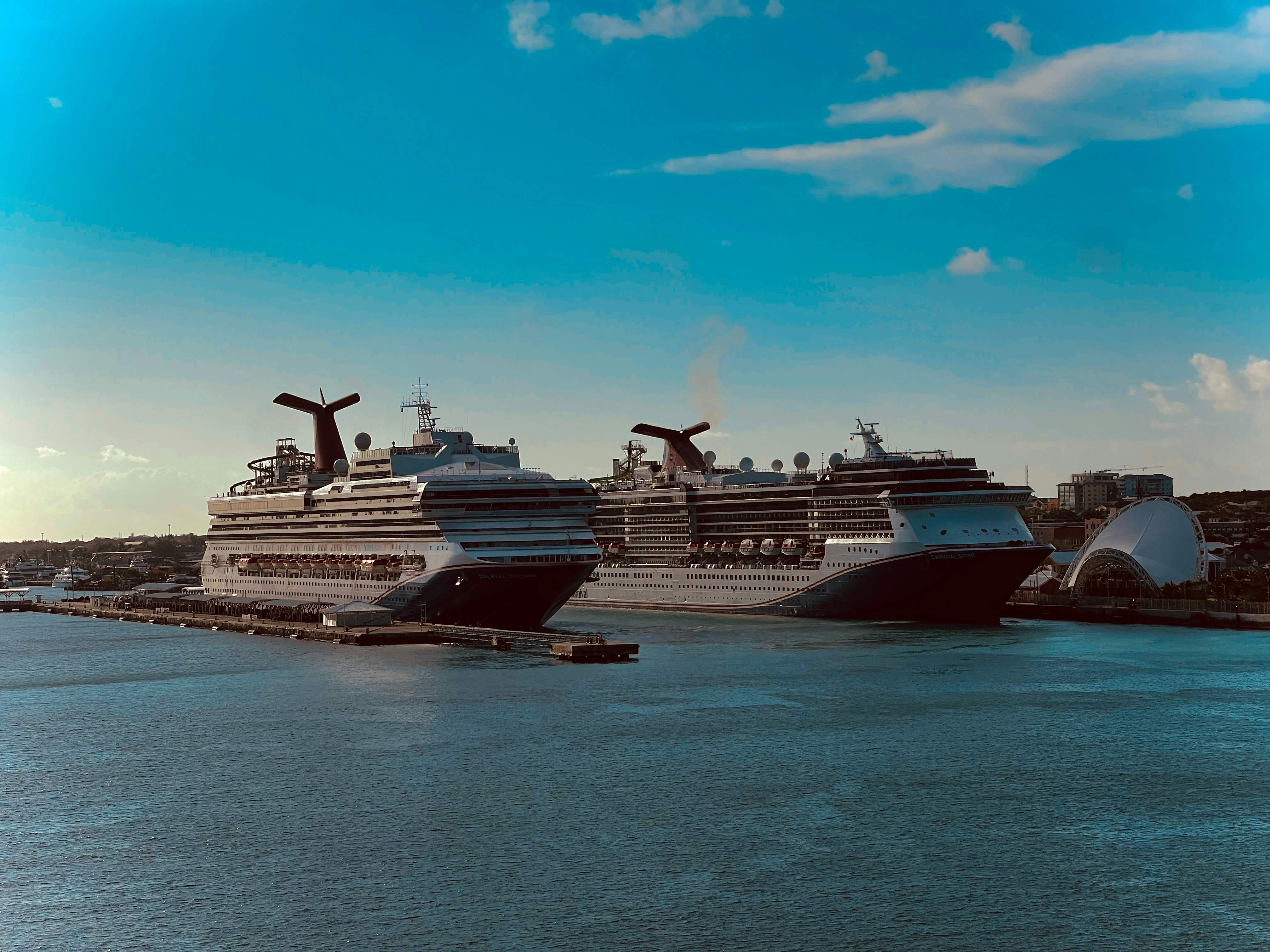 Two large cruise ships docked in a serene harbor under a clear blue sky.