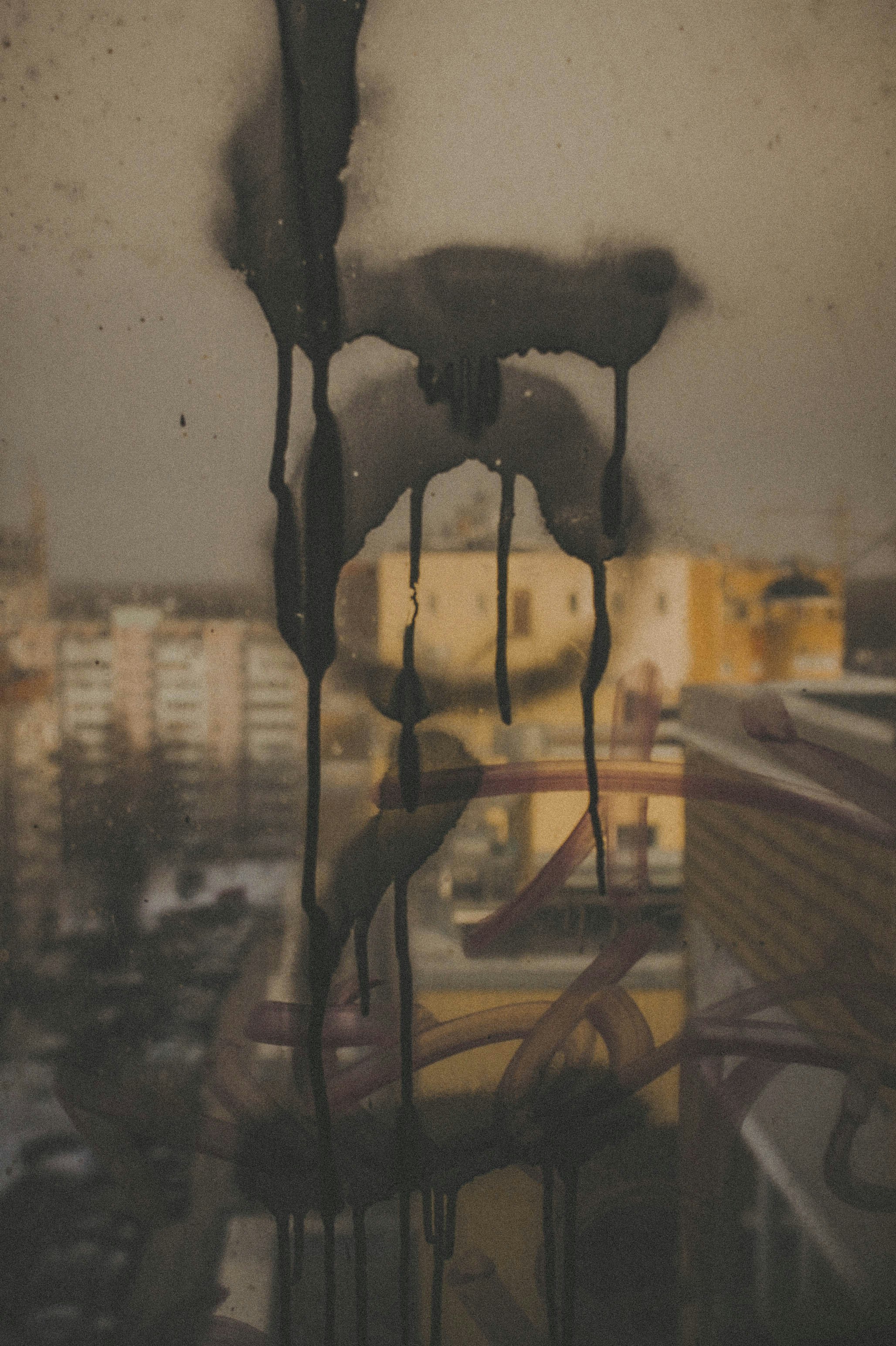 Dripping graffiti obscures a cityscape view through a foggy window, highlighting the contrast between urban decay and vibrant expression.