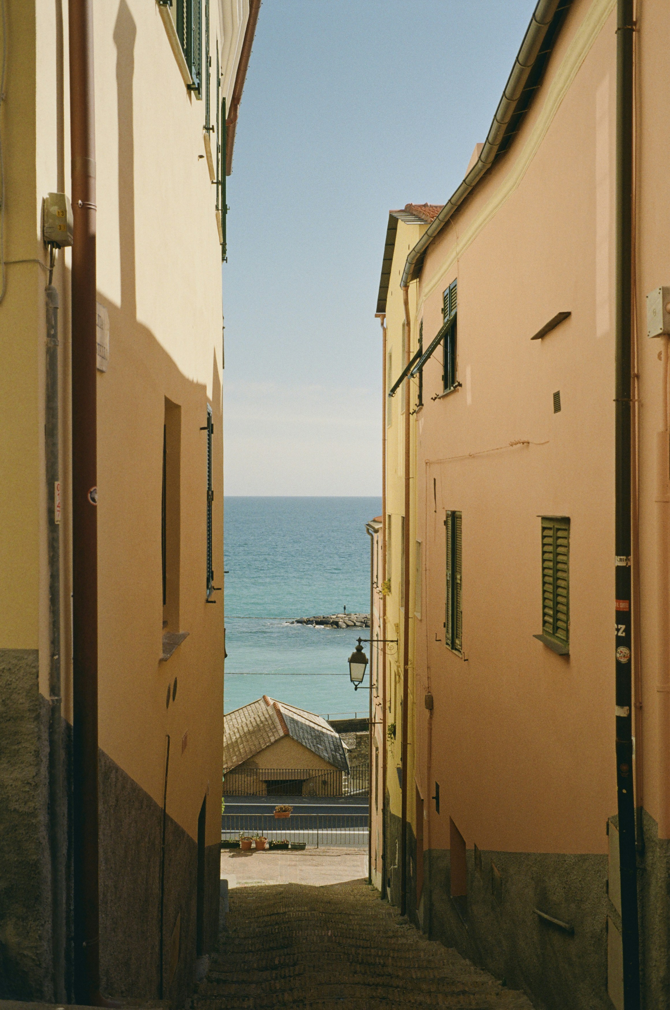 Alleyway between pastel buildings leading to the Ligurian Sea under a clear sky.