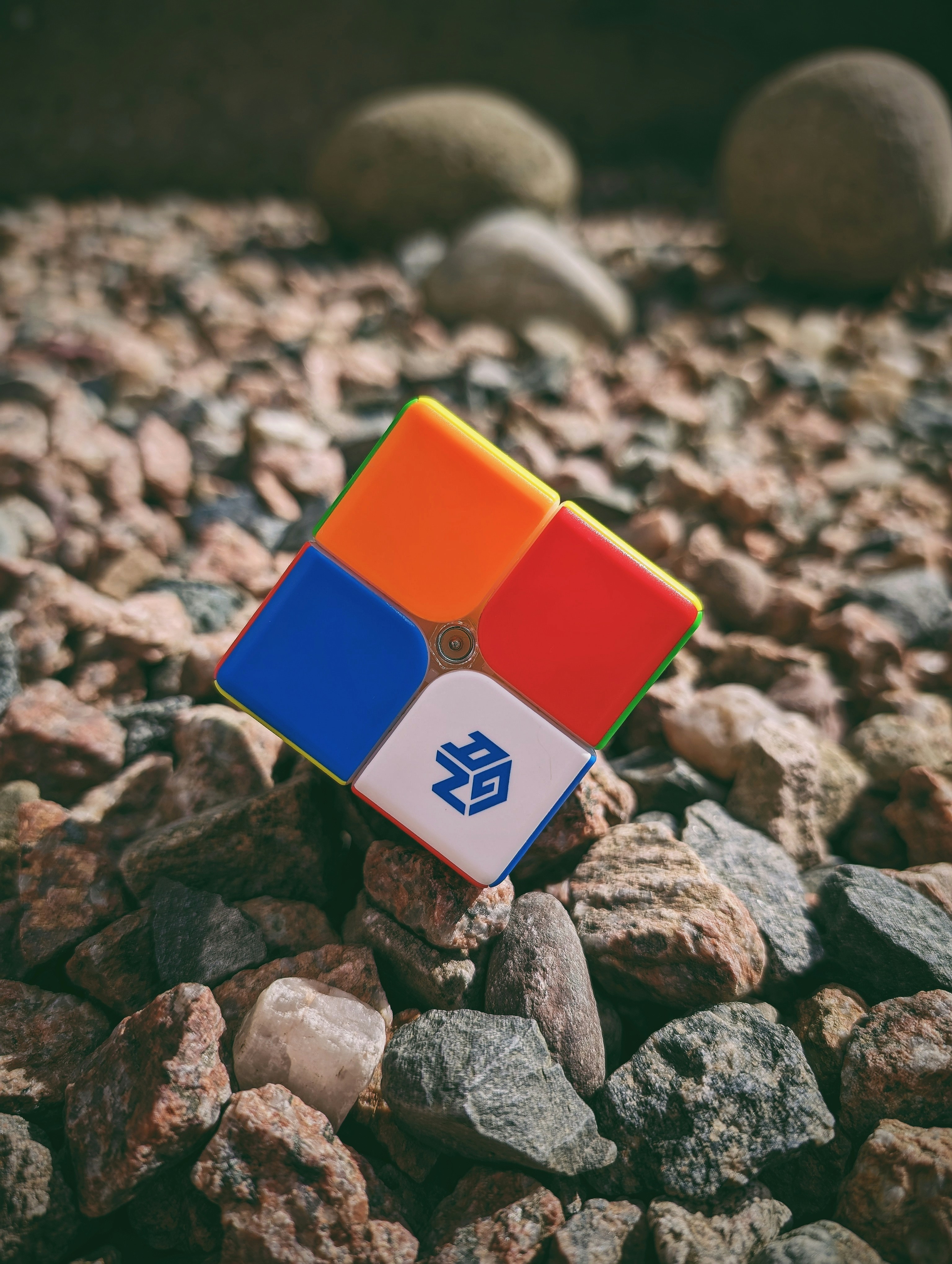 A vibrant Rubik's cube stands out against a textured backdrop of pebbles and stones, showcasing its playful colors and design.