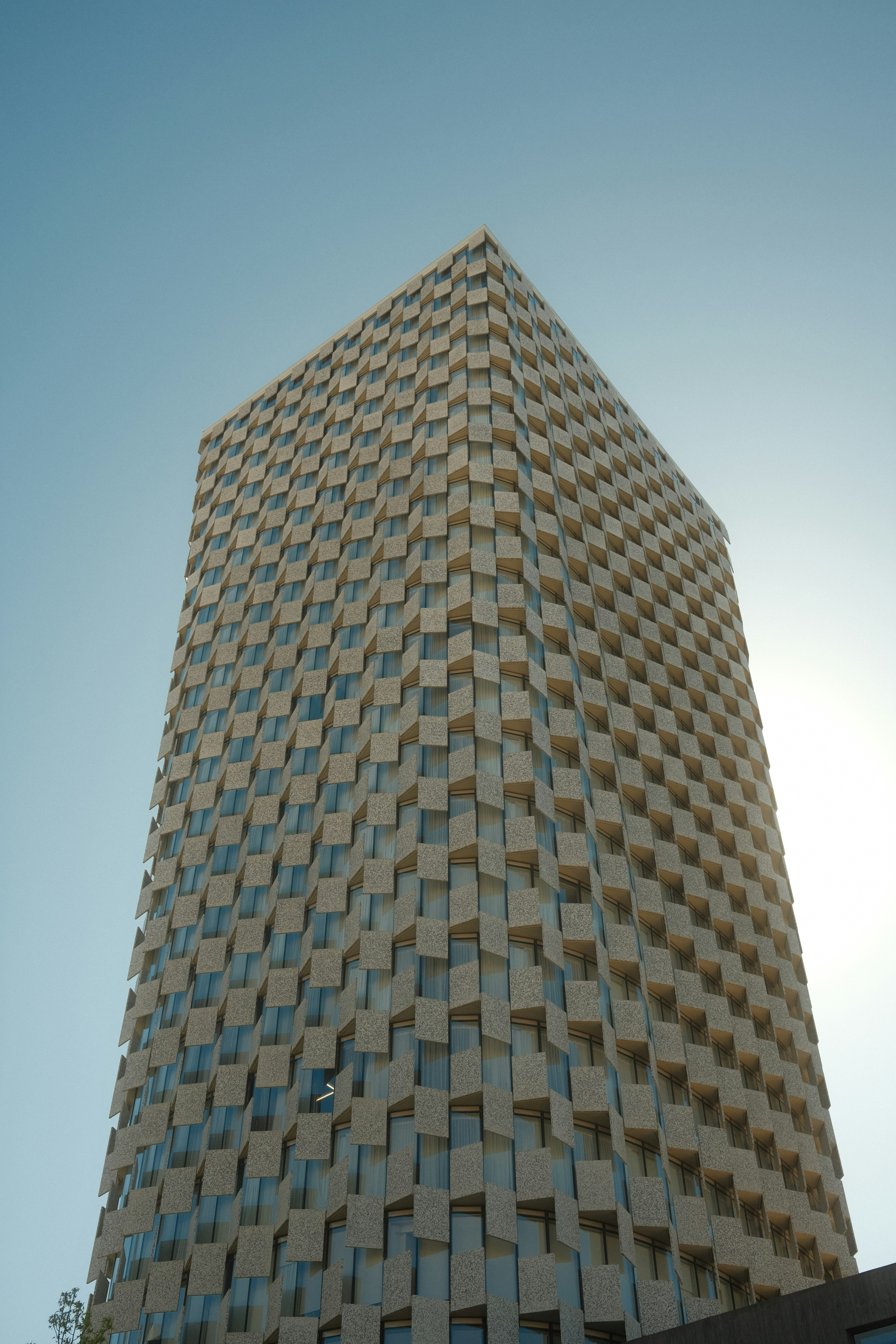 Architectural photograph of a tall high-rise with a grid-like, cube-pattern facade towering against a clear sky.