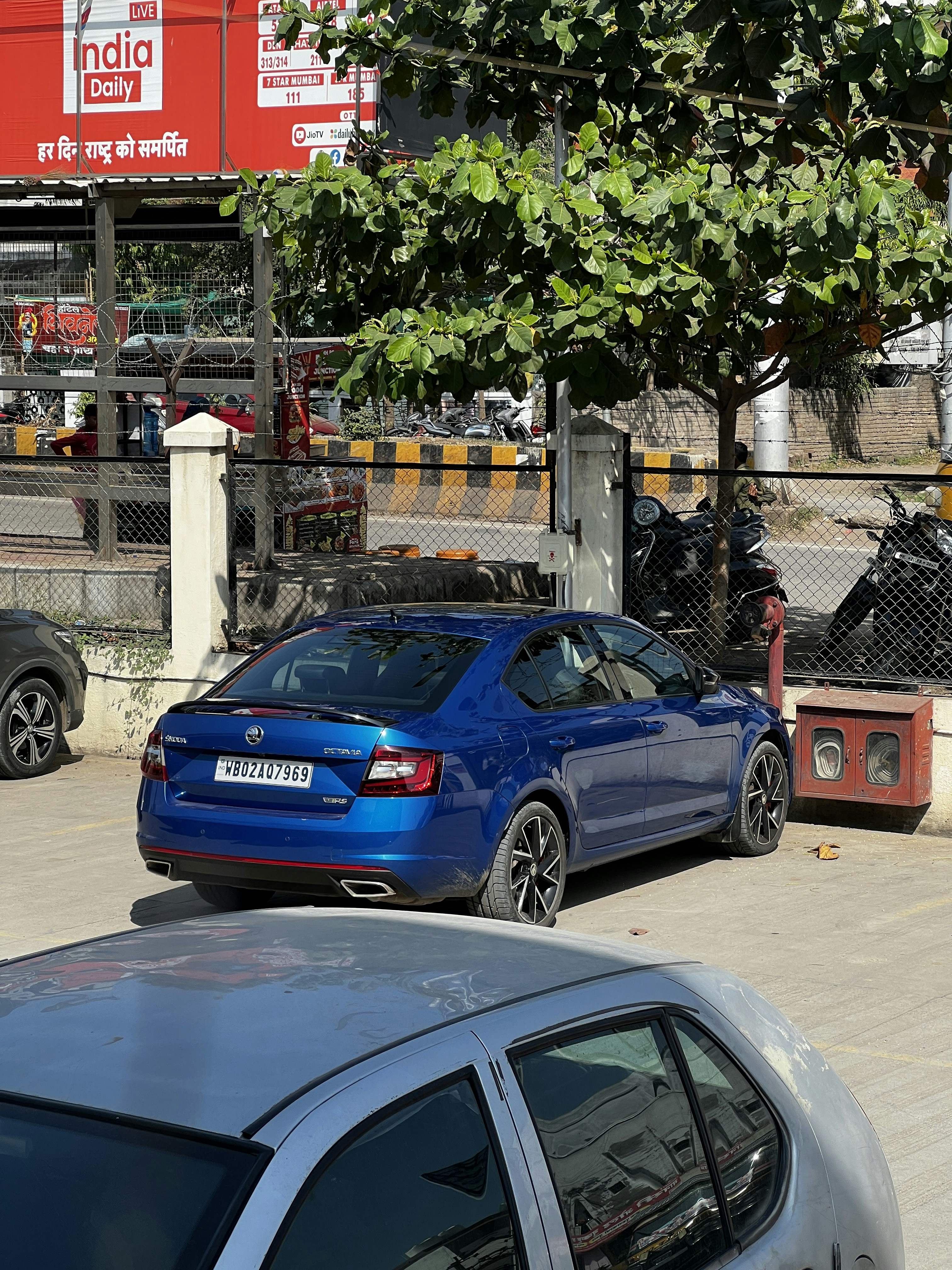 Azure Sedan Anchors a Sunlit Urban Parking Lot Framed by Foliage and Barriers