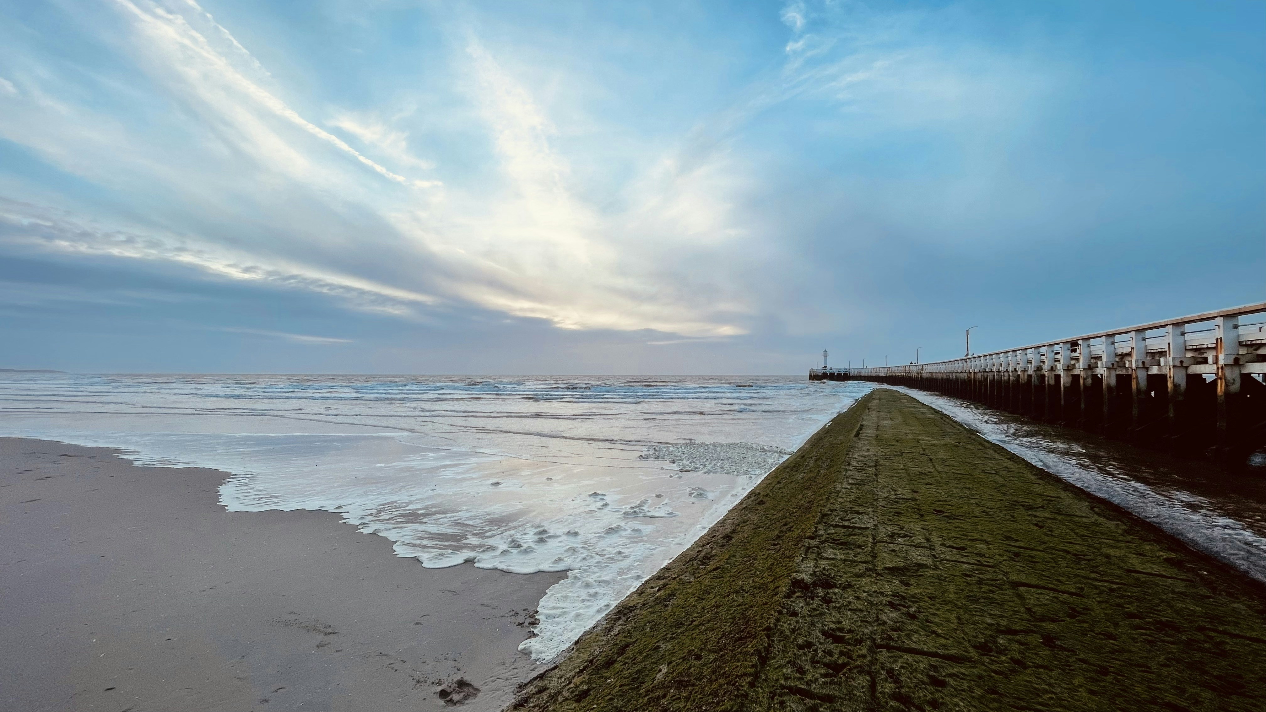 Expansive ocean meeting a grassy embankment under a dynamic, cloud-streaked sky.