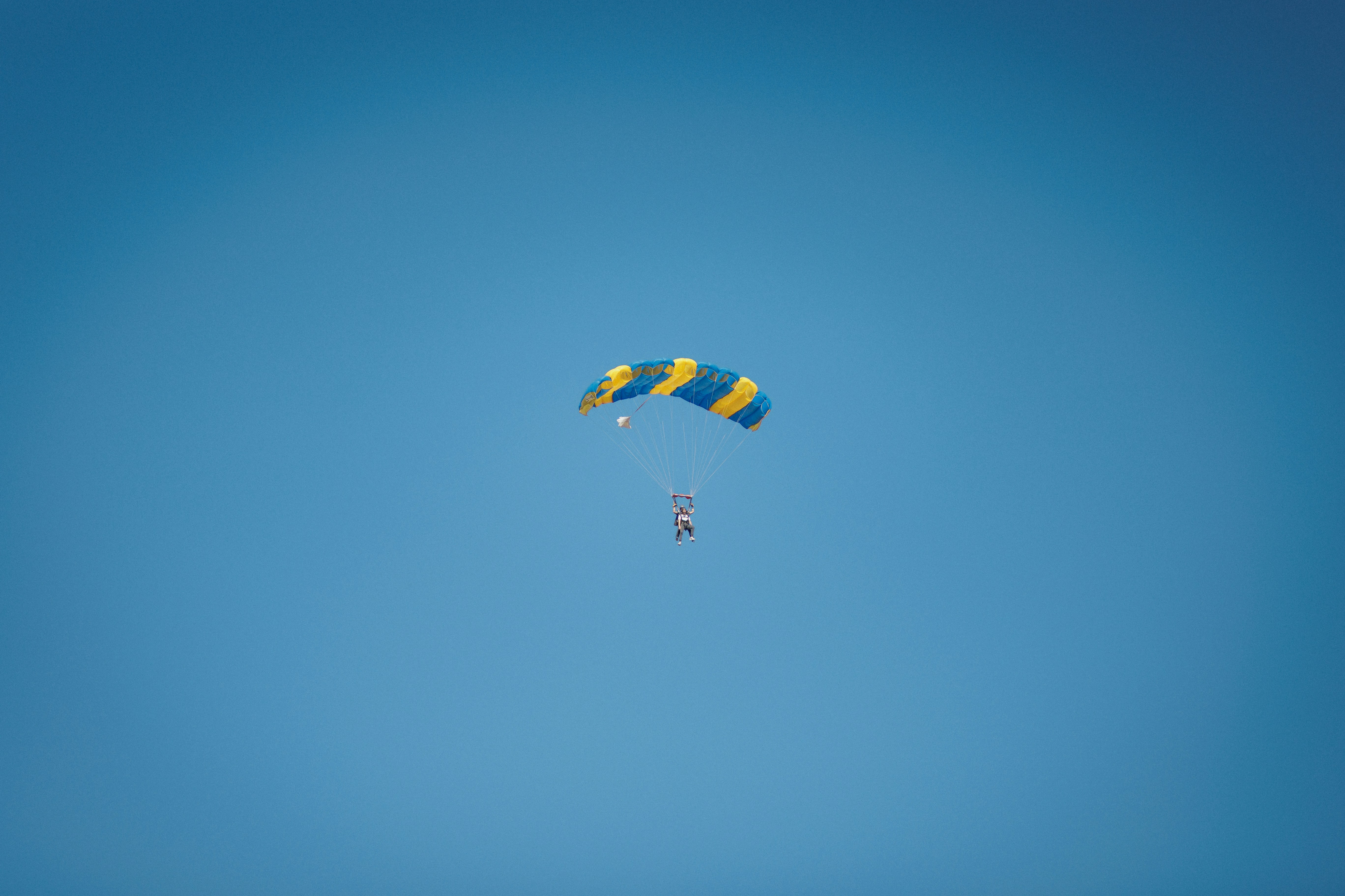 Cobalt Skyward: A lone paraglider drifts beneath a striped blue-yellow canopy