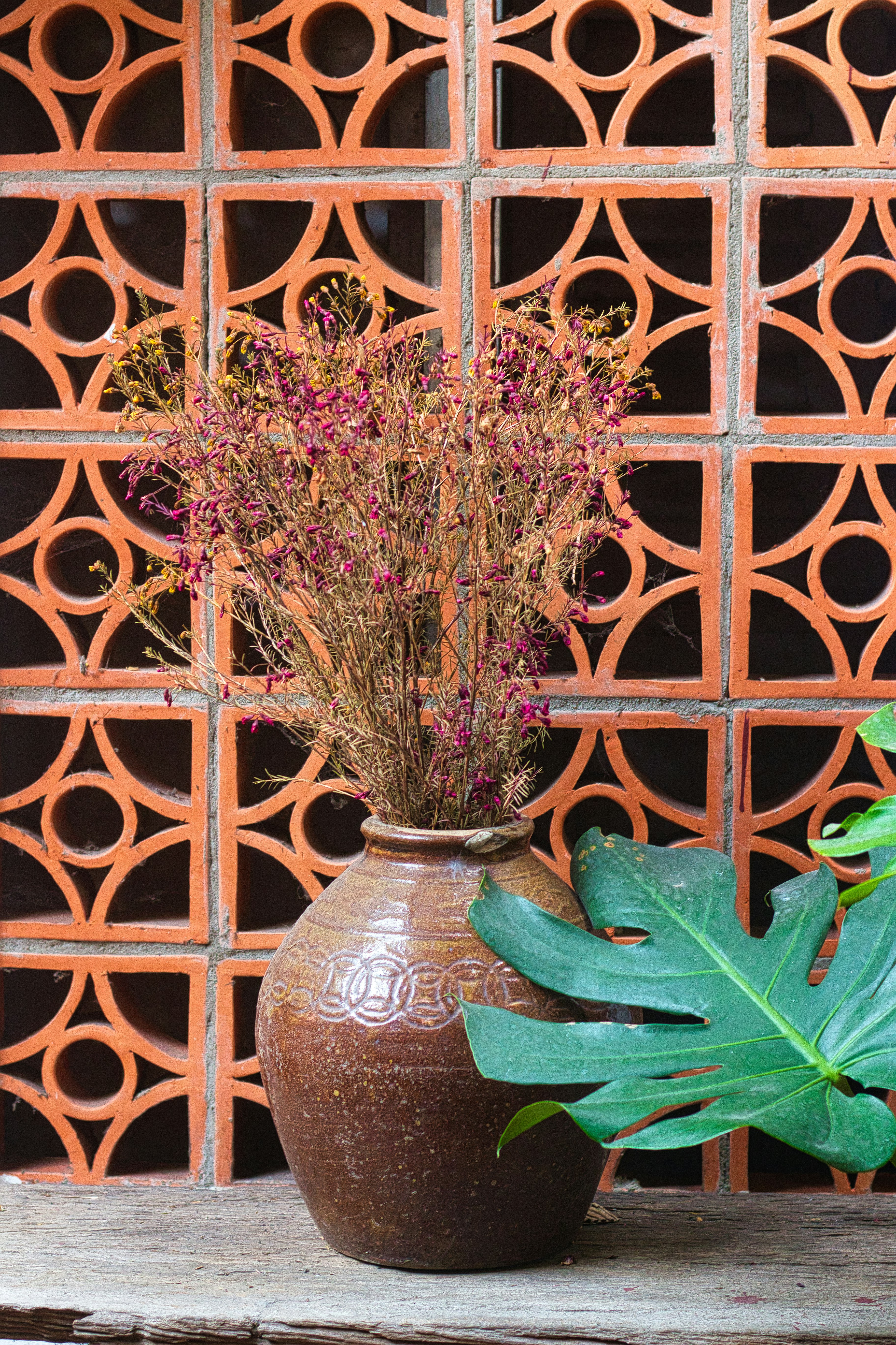 Dried Bouquet in a Weathered Ceramic Jar Against a Circular Terracotta Lattice Wall