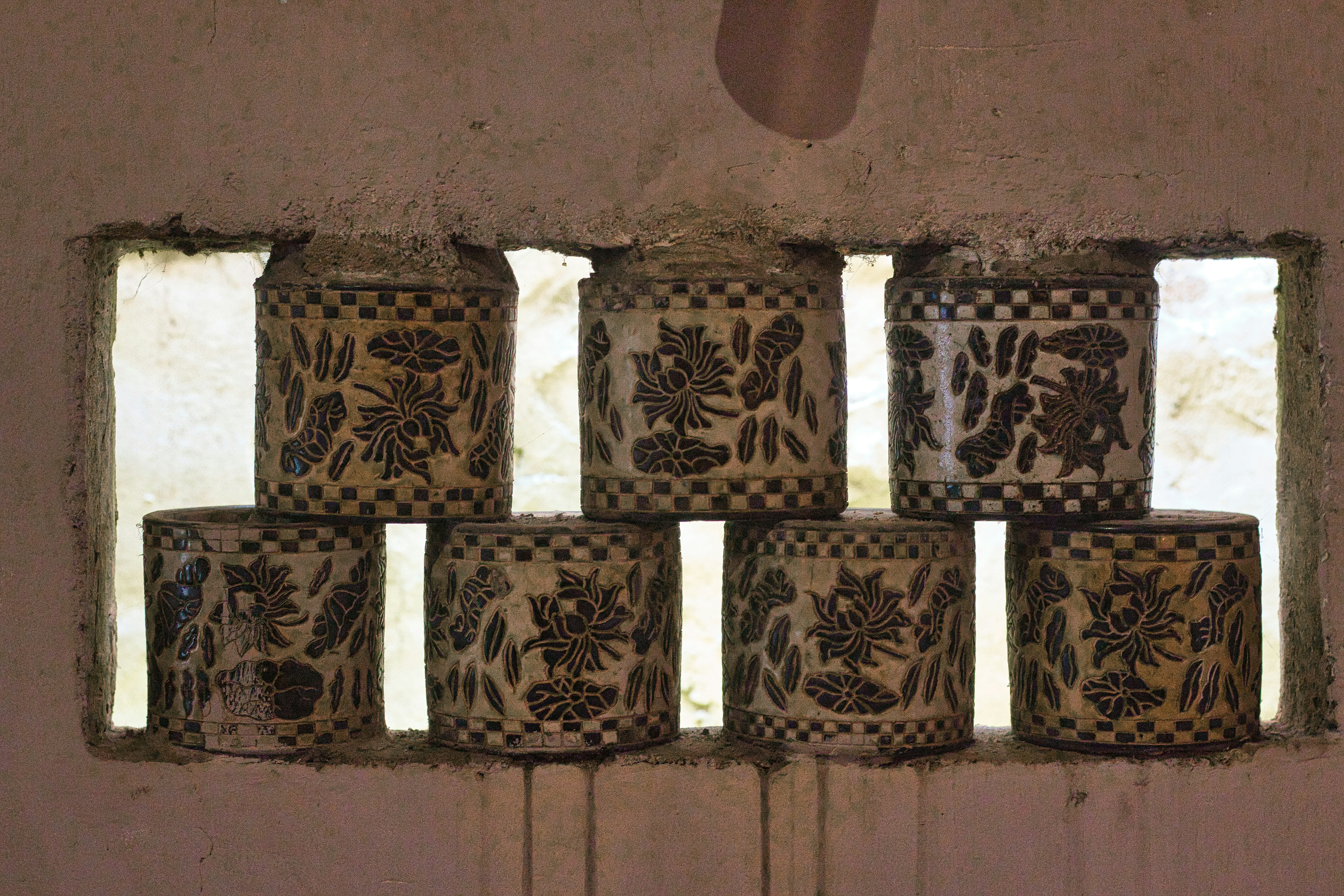 Six floral ceramic jars clustered in a sunlit brick alcove