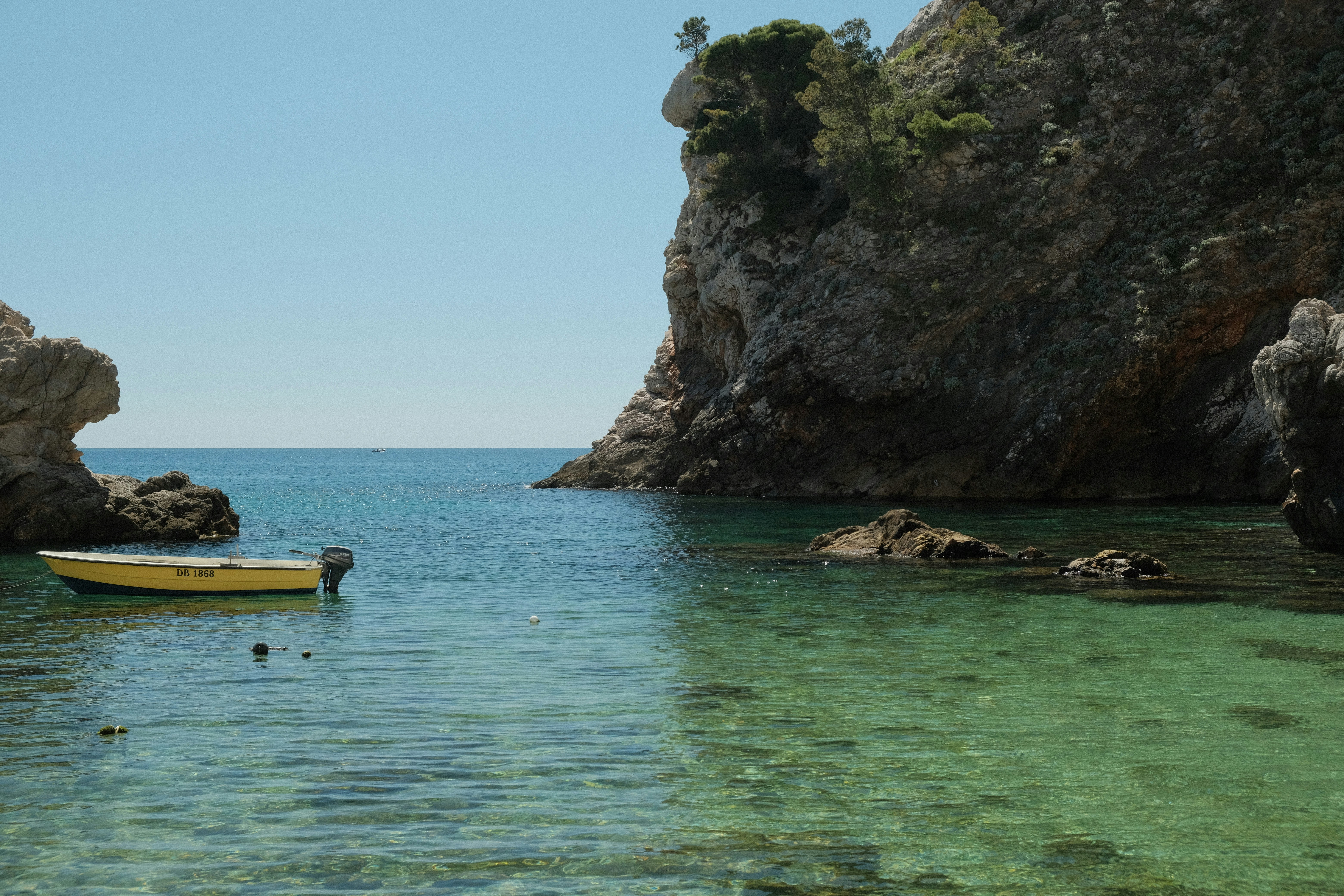 Quiet Turquoise Cove: A Yellow Boat Between Emerald Water and Rugged Cliffs