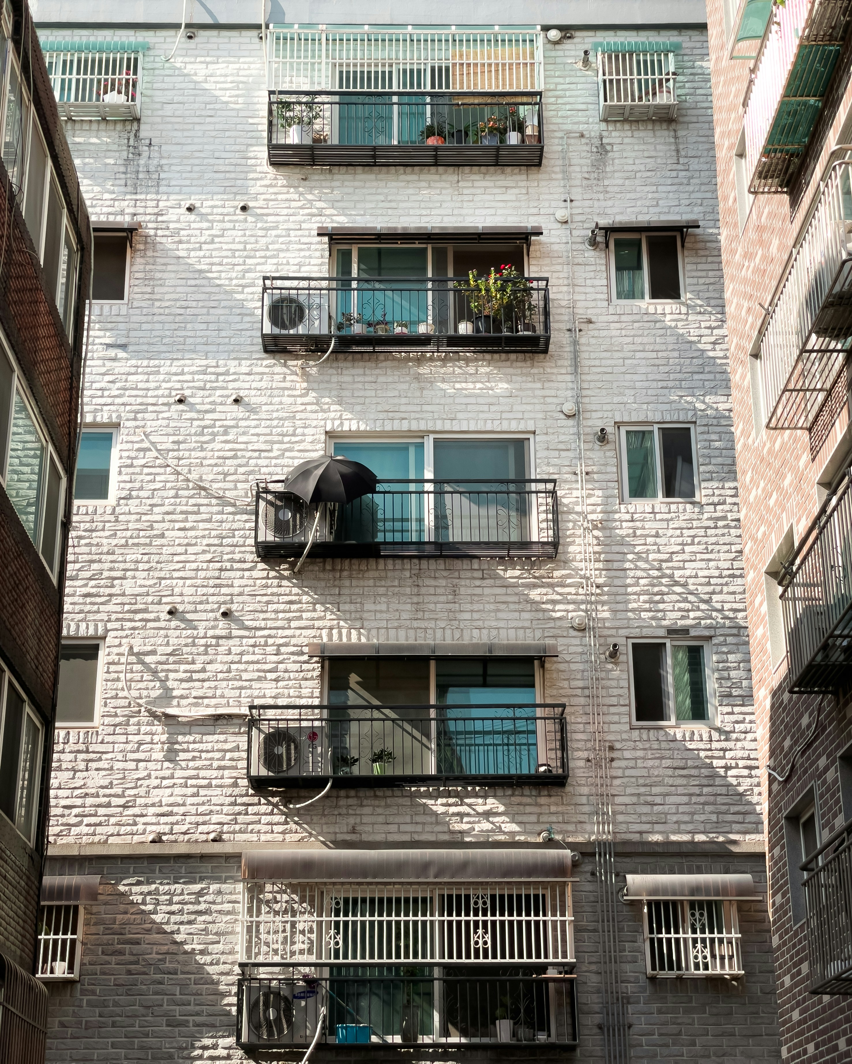 Umbrella Anchored on a Sunlit City Brick Balcony Row