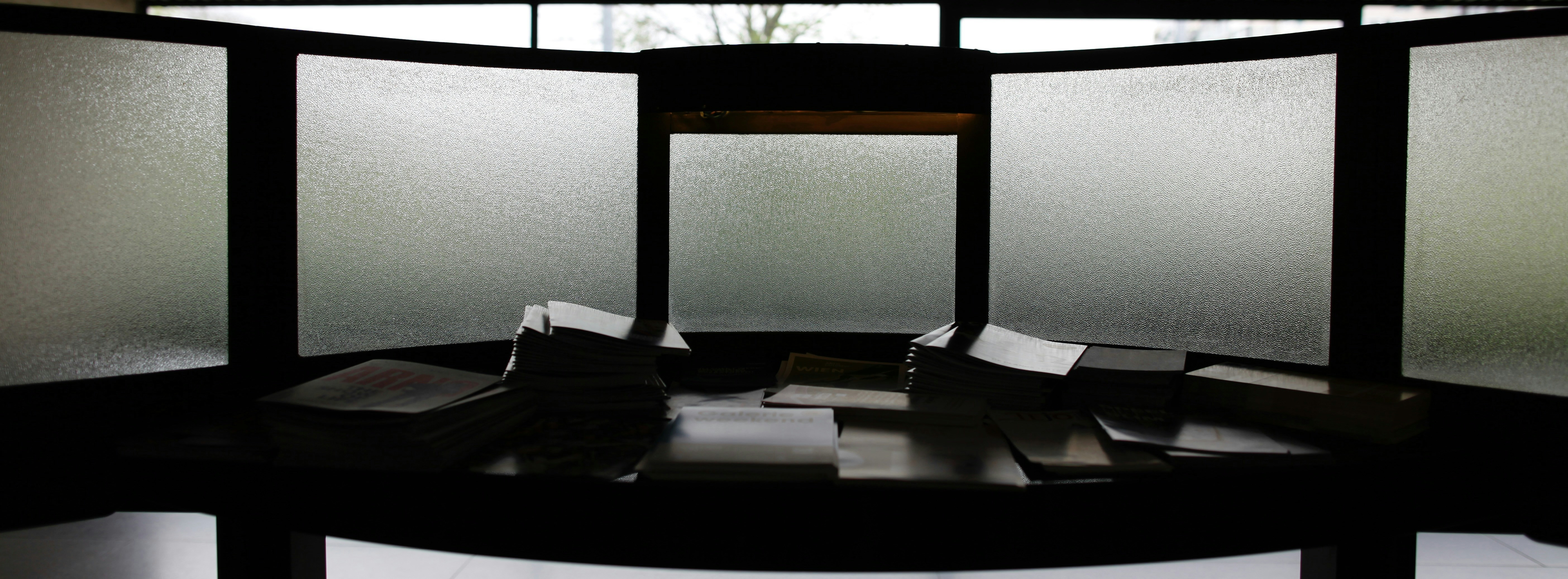 Silhouetted desk surrounded by frosted glass panels, with scattered documents creating a sense of quiet contemplation.