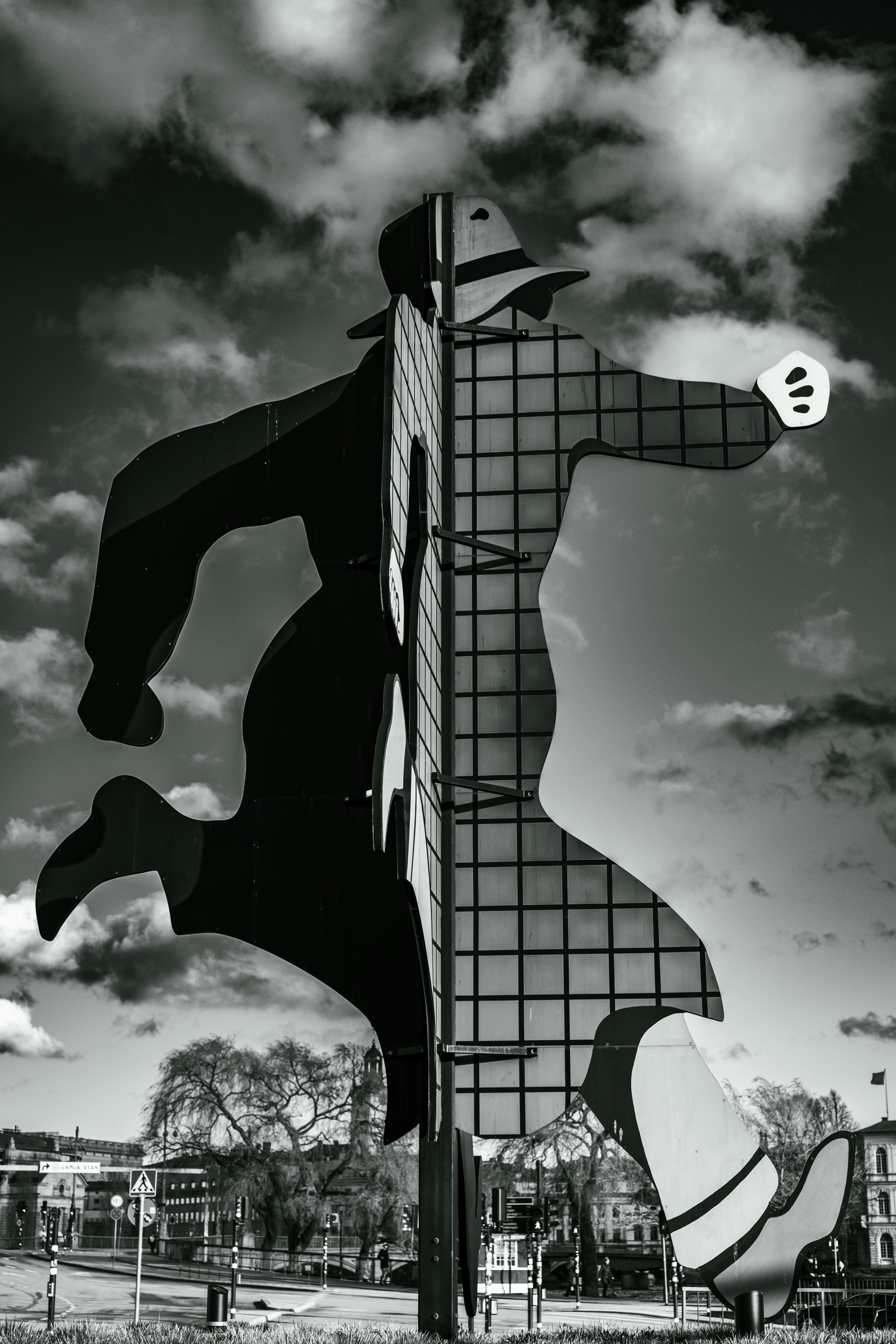 A large, abstract sculpture of a walking figure, rendered in black and white, set against a dramatic sky with clouds.