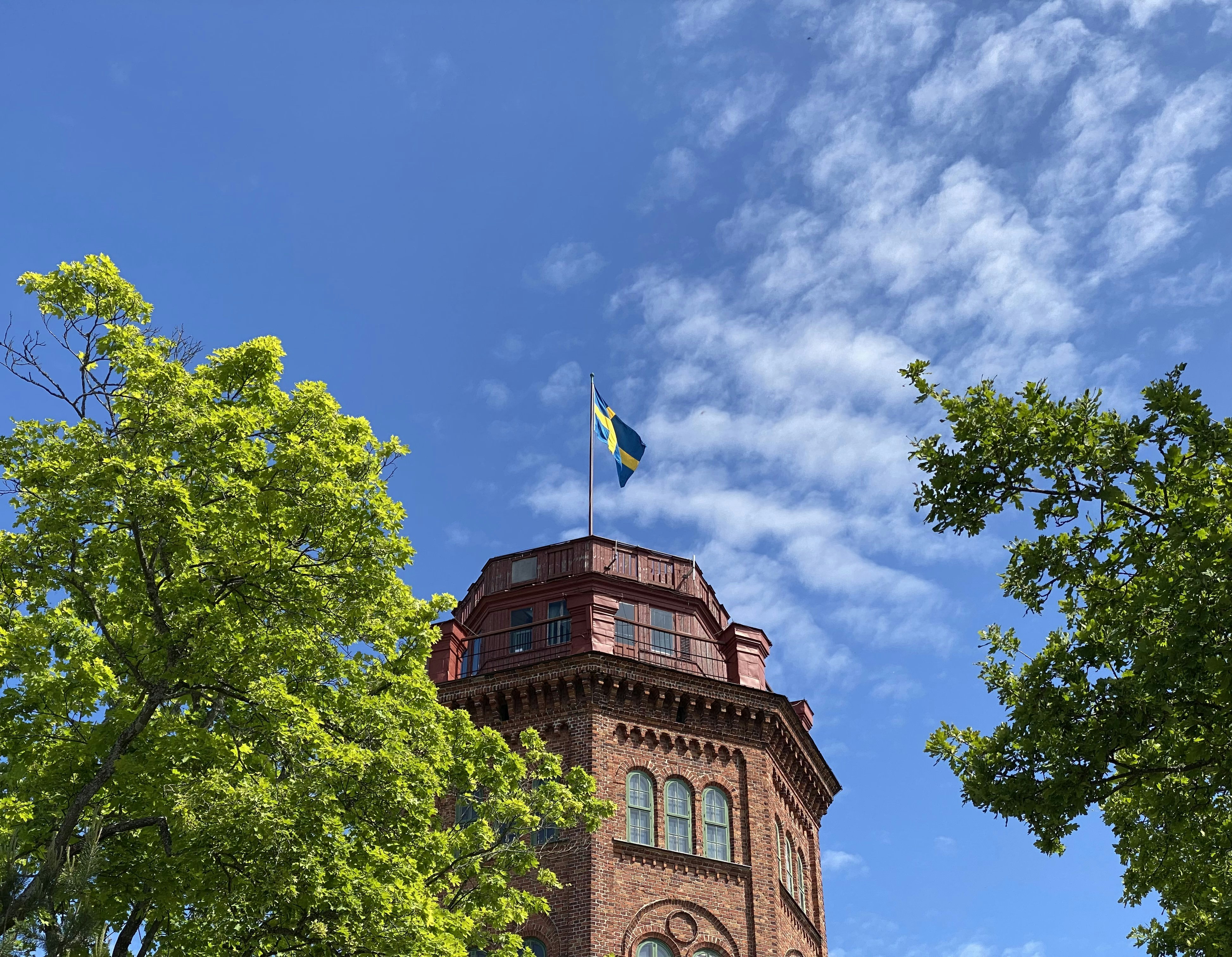 Flag atop a red-brick clock tower beneath a crisp Nordic sky
