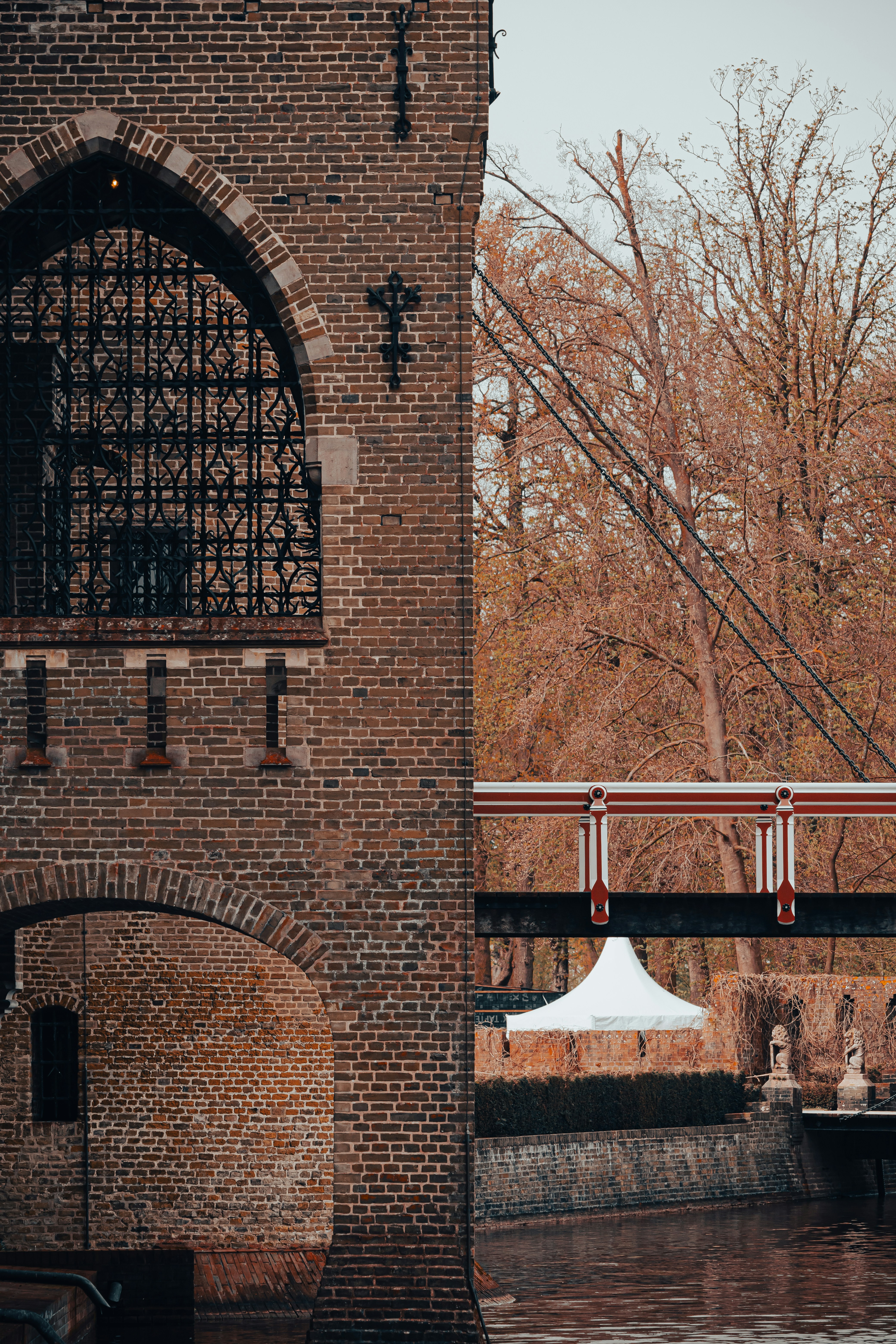 Archway Portrait: Brick Gothic, Iron Grille, and a Riverside Bridge in Autumn Light