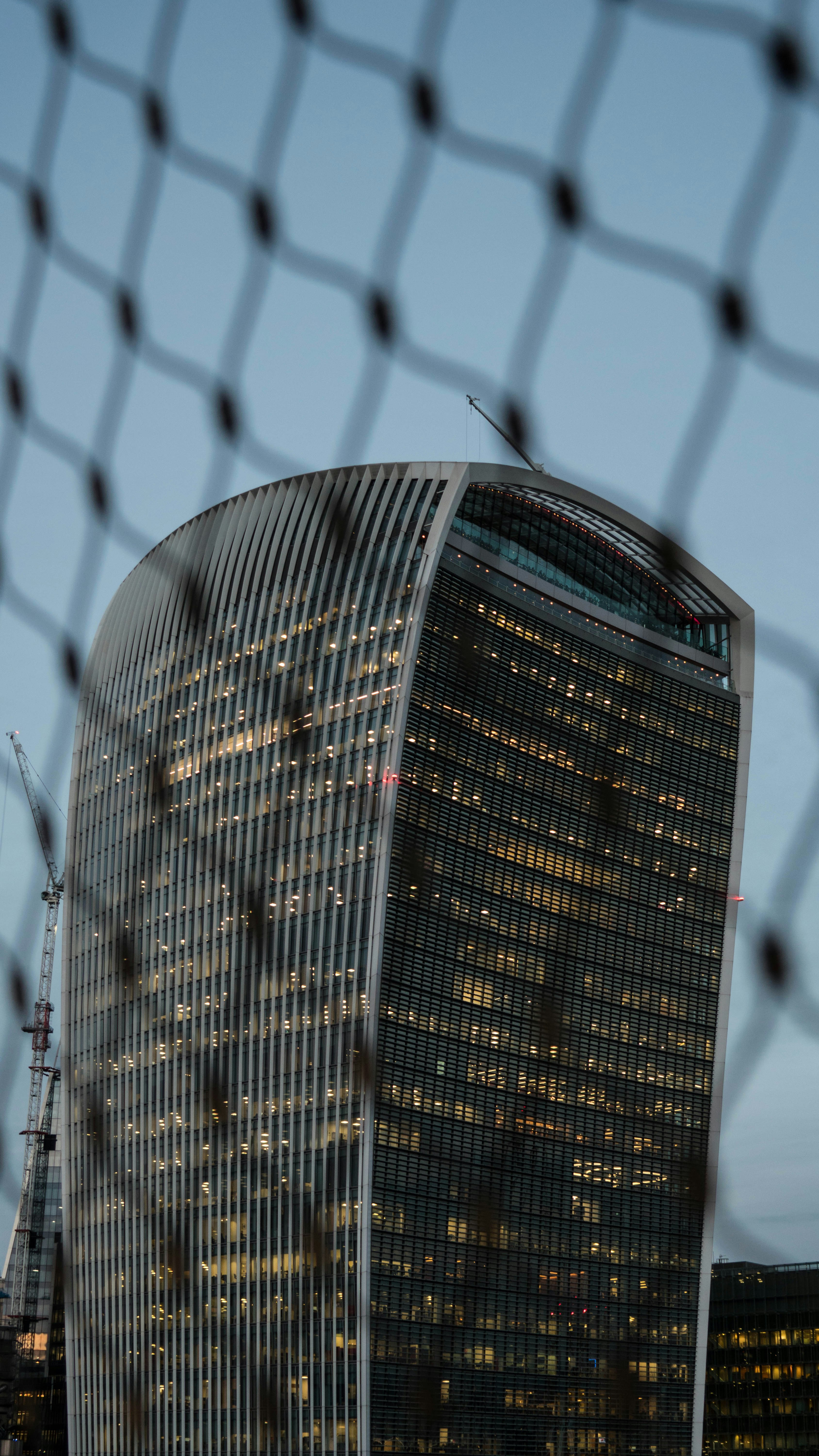 Framed Curve: The Looped Glass Tower Rising Behind a Mesh Fence
