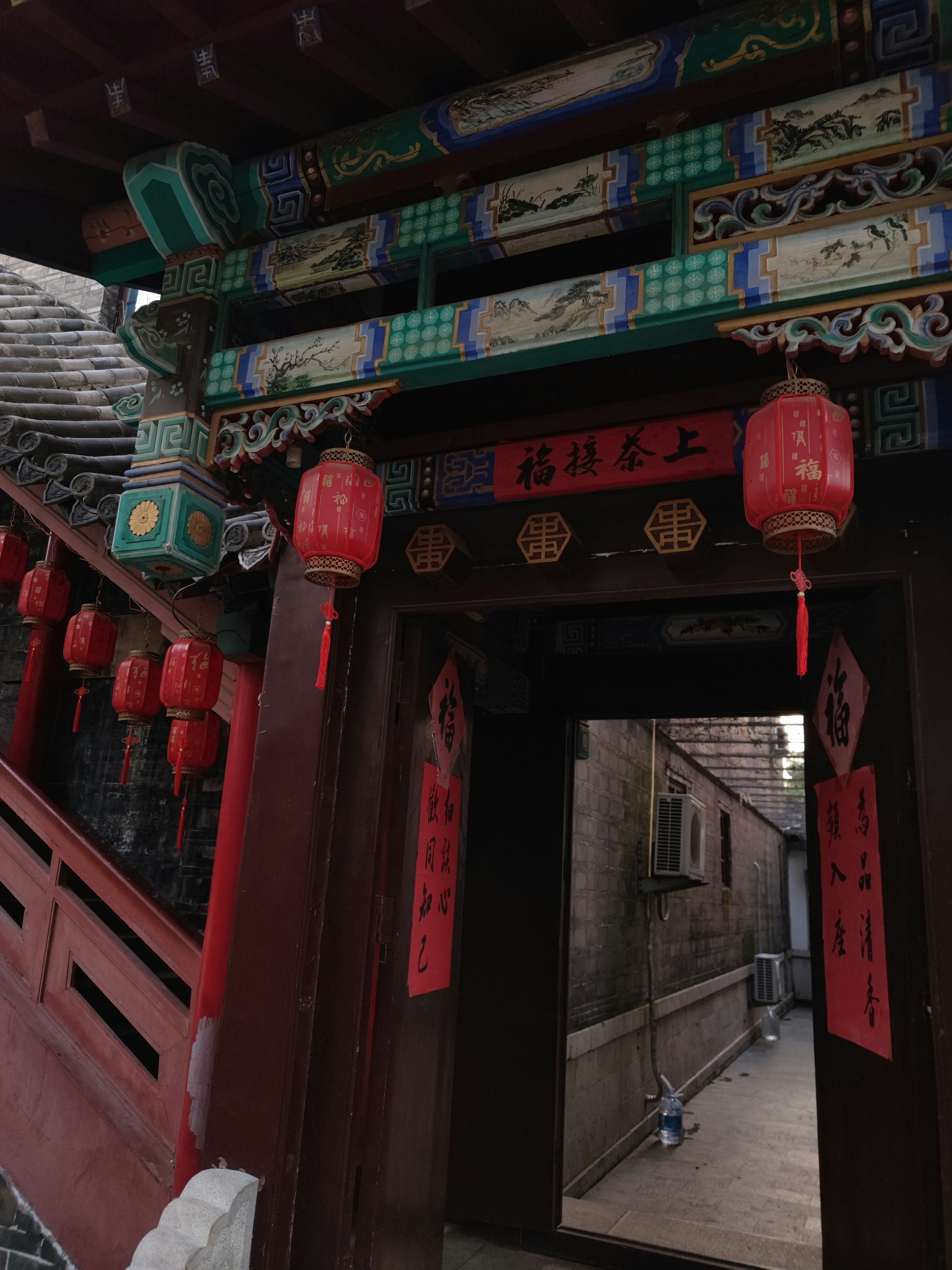 Traditional Chinese temple doorway framed by red lanterns and ornate painted beams, with a narrow passage visible beyond.