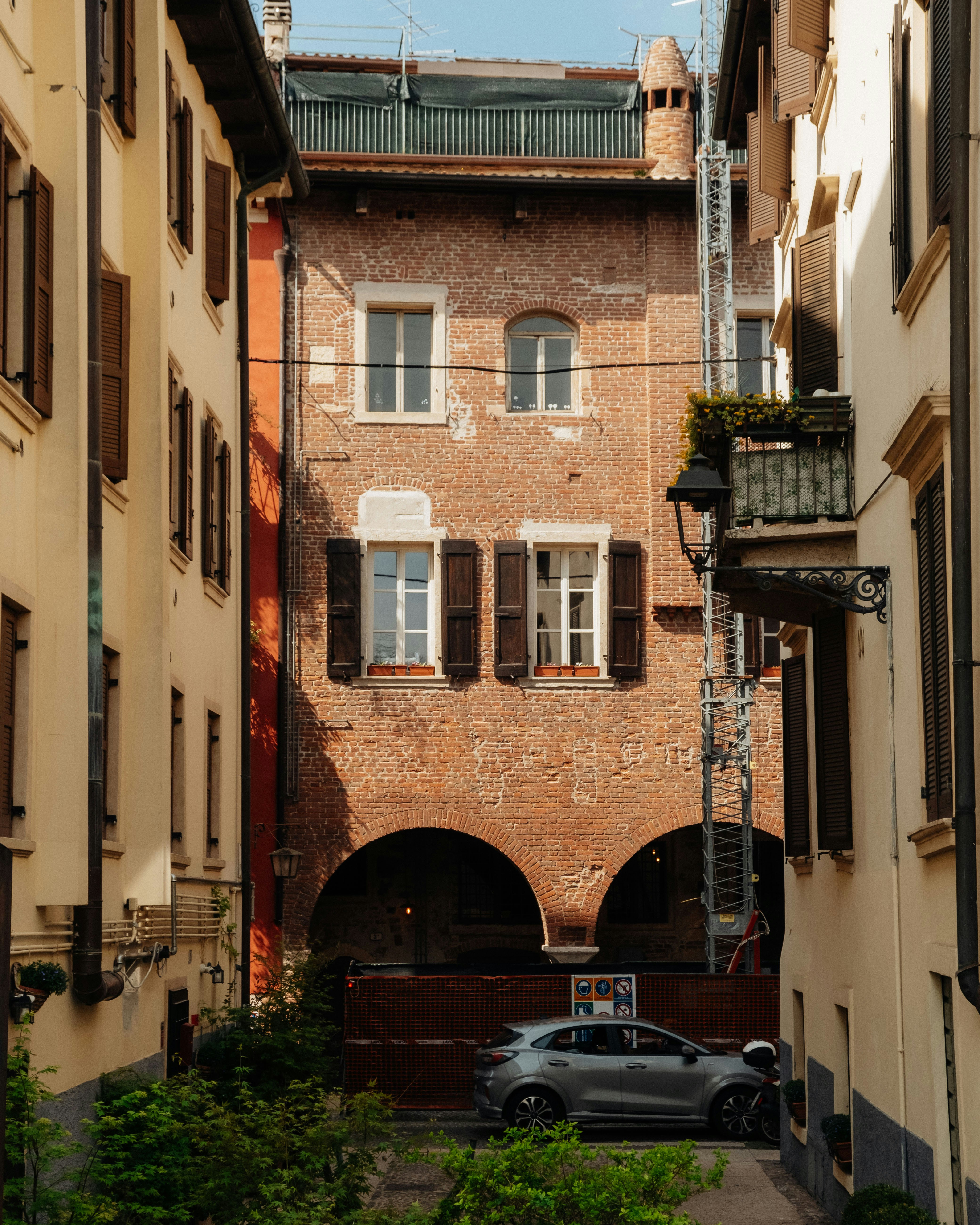 Sunlit Brick Courtyard: Arches, Windows, and a Silent Car