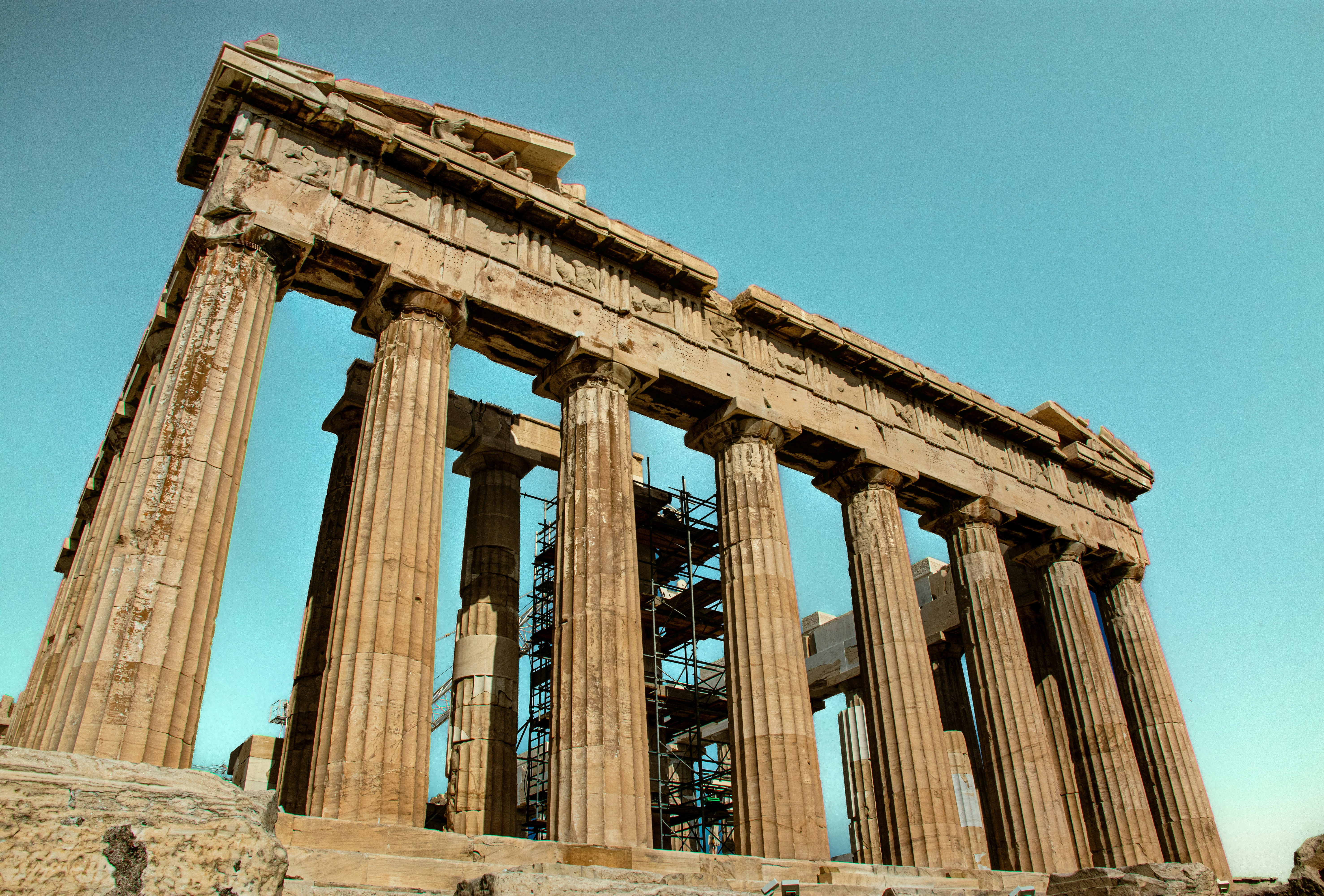 Ancient Parthenon columns rise majestically against a clear blue sky, with scaffolding hinting at ongoing restoration.
