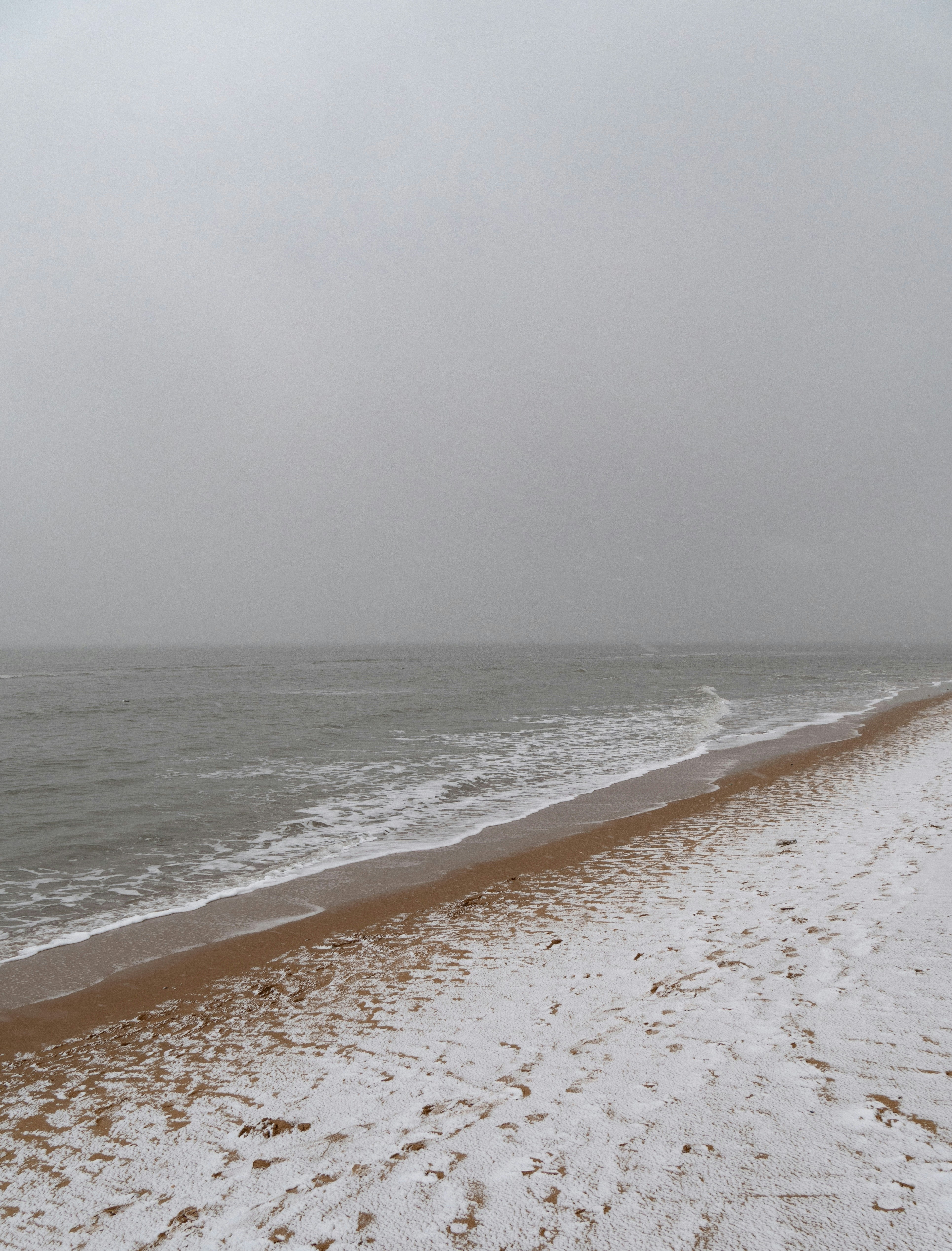 A beach covered in snow next to the ocean photo – Free Grey Image on ...