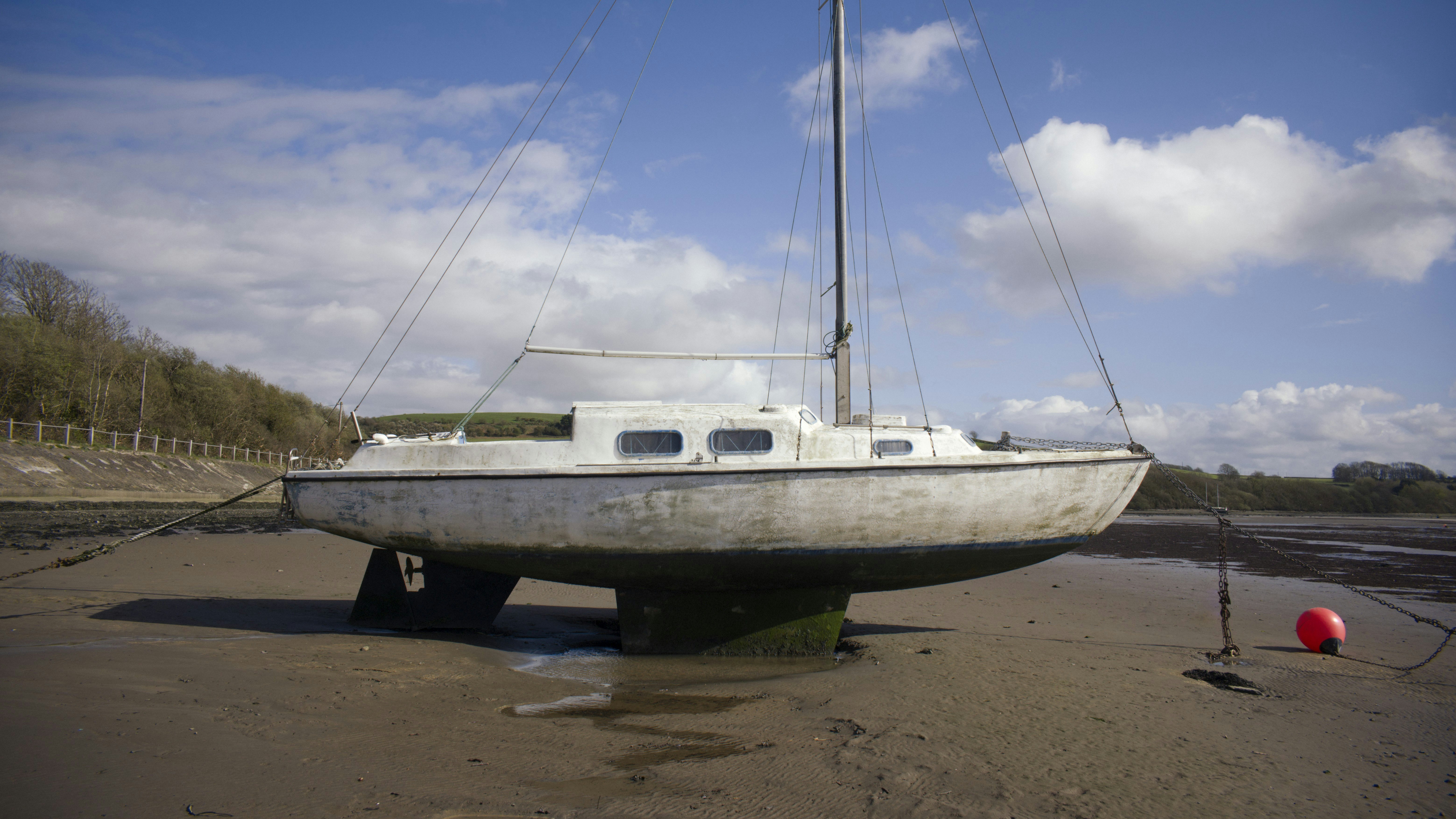 Beached Sloop at Low Tide: Weathered Hull on Mud Flats with a Red Buoy