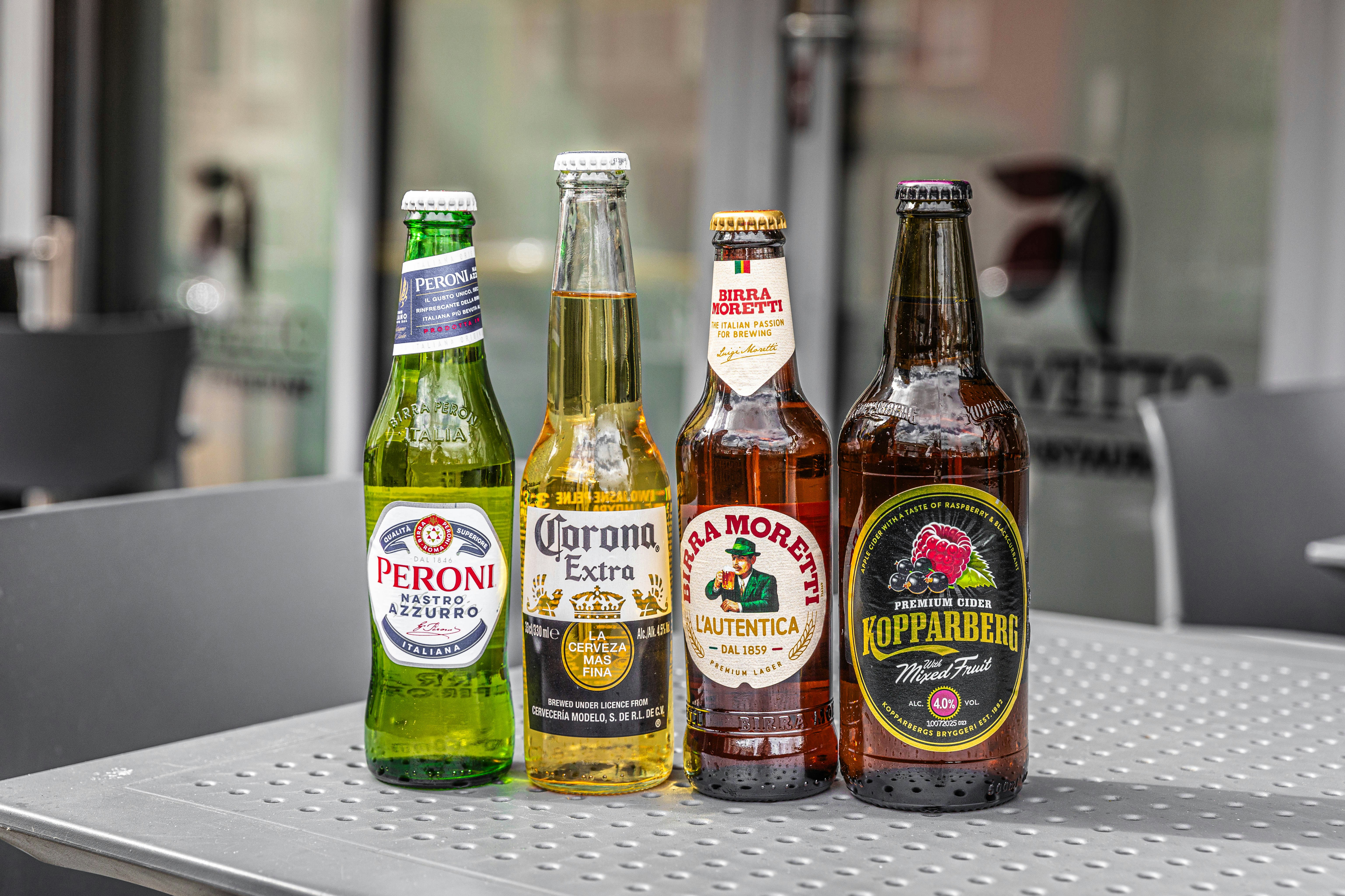 Row of Four Beer Bottles on a Sunlit Perforated Table