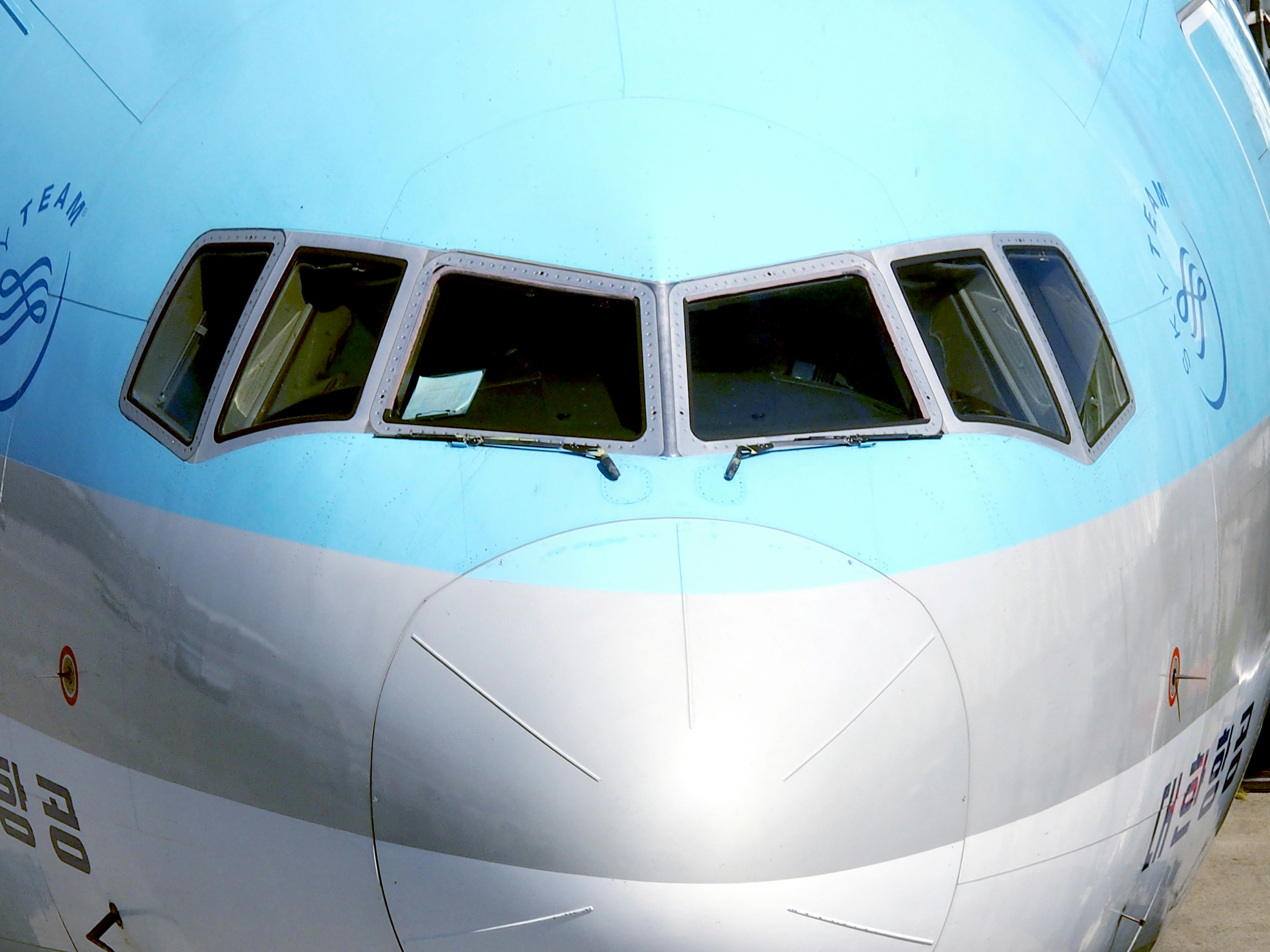 Front-on shot of a jet nose and cockpit windows with blue-silver livery, highlighting symmetry. The image emphasizes the aircraft's forward profile and glossy metal surfaces.