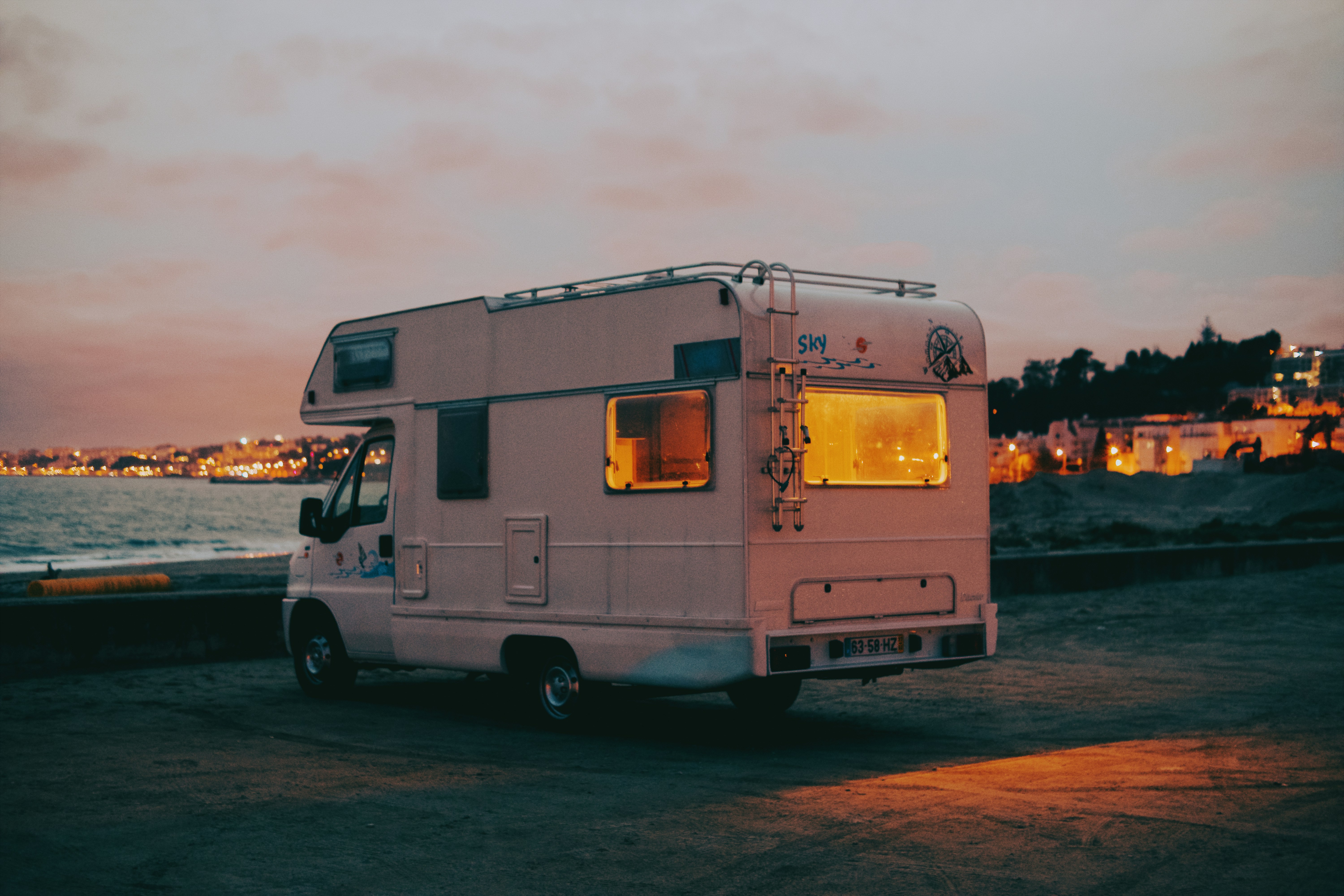 Caravan illuminated at dusk near the ocean with a vibrant sunset sky.