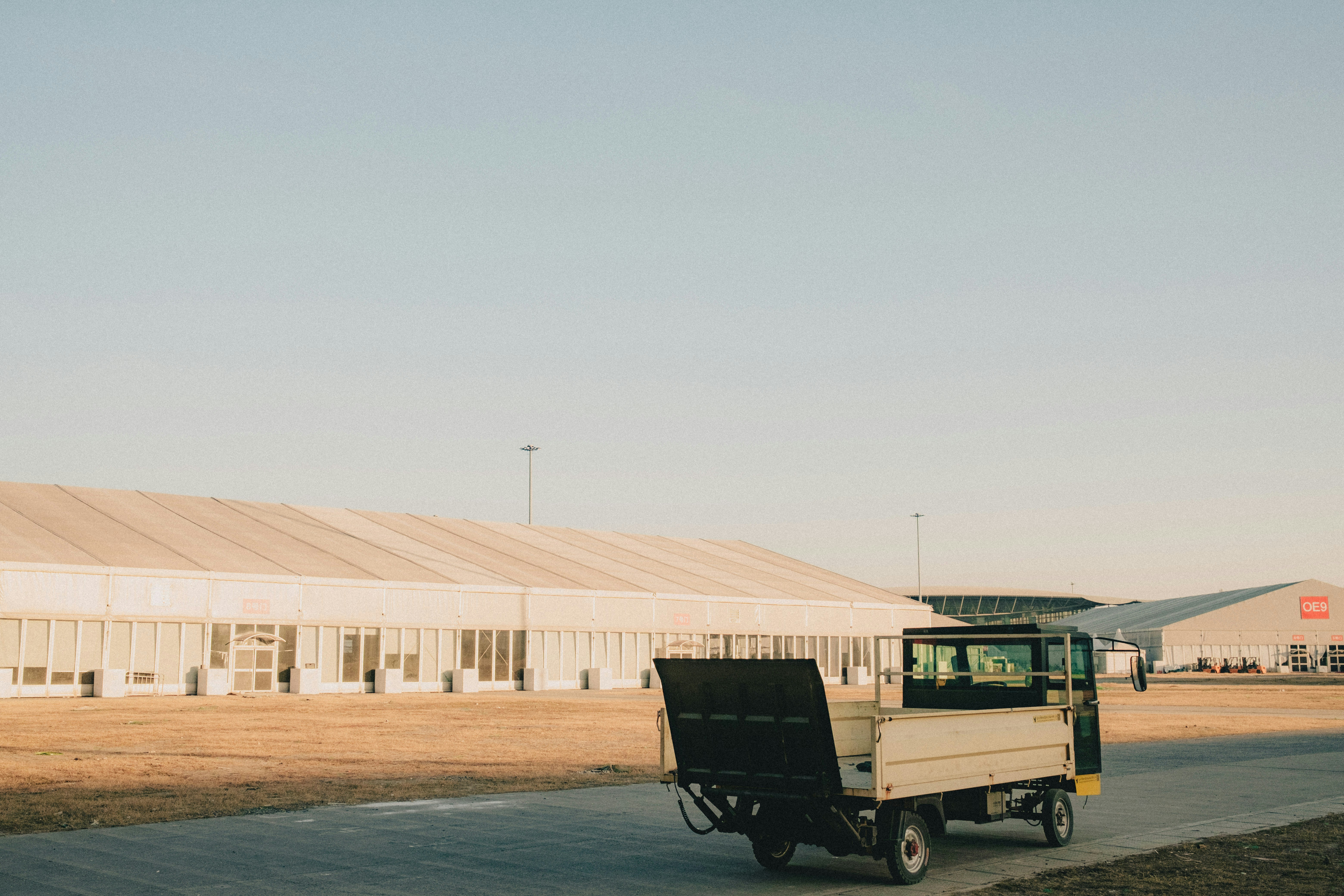 Small truck on a road beside a large industrial building under clear skies.
