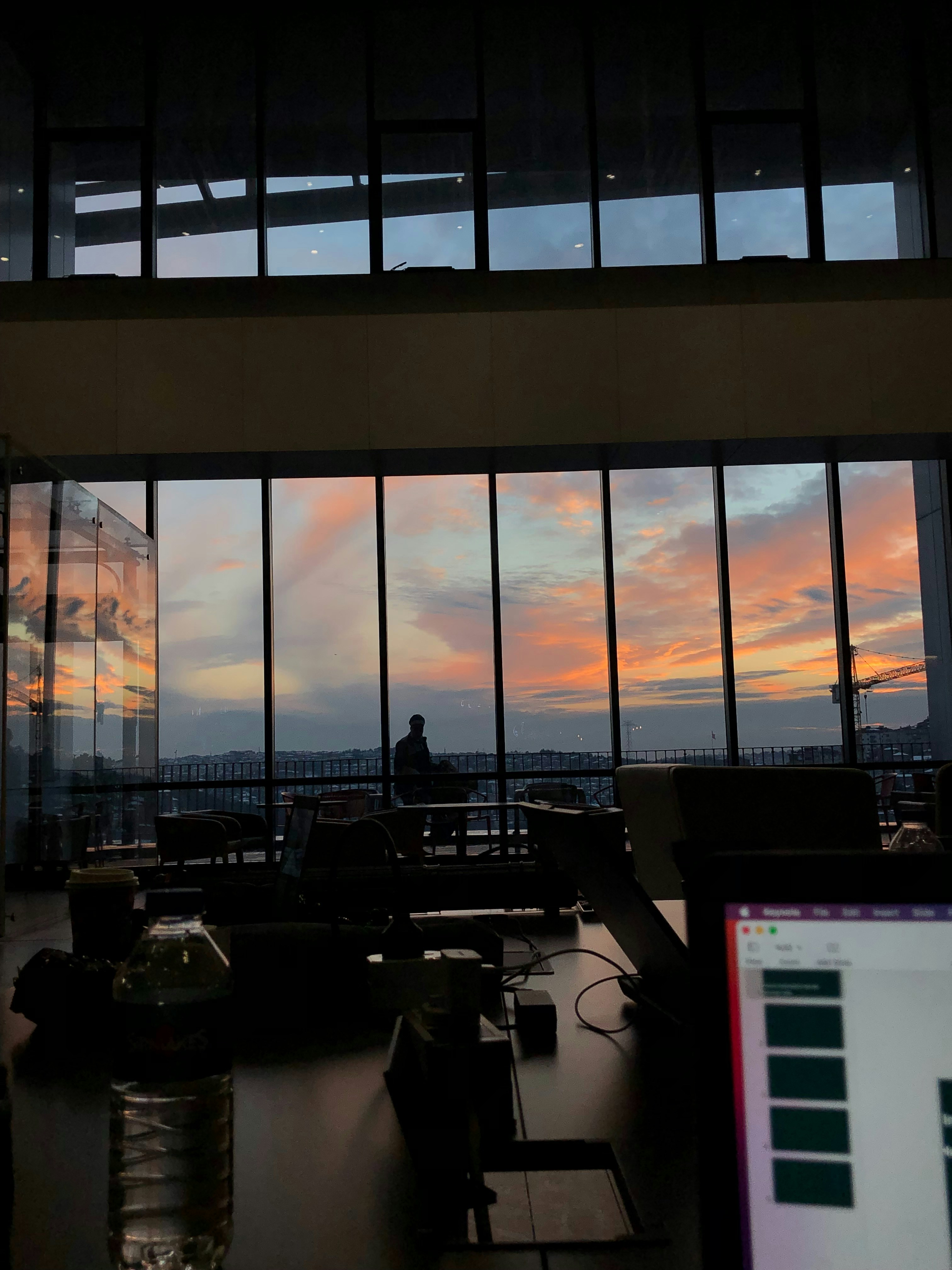 Silhouette at Dusk: Office Window Framing an Orange-Glow Cityscape