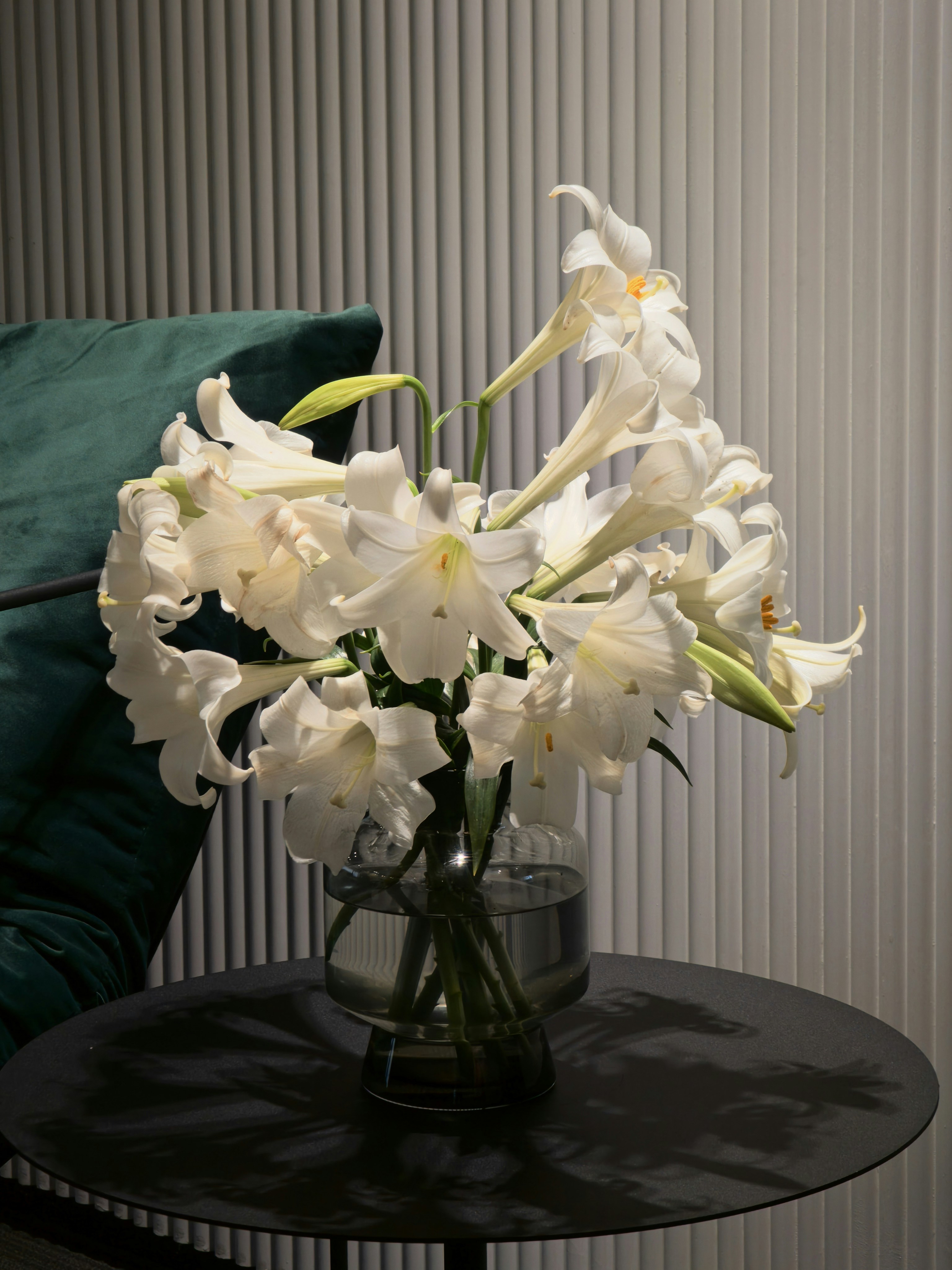 White lilies on a dark glass vase against ribbed wall
