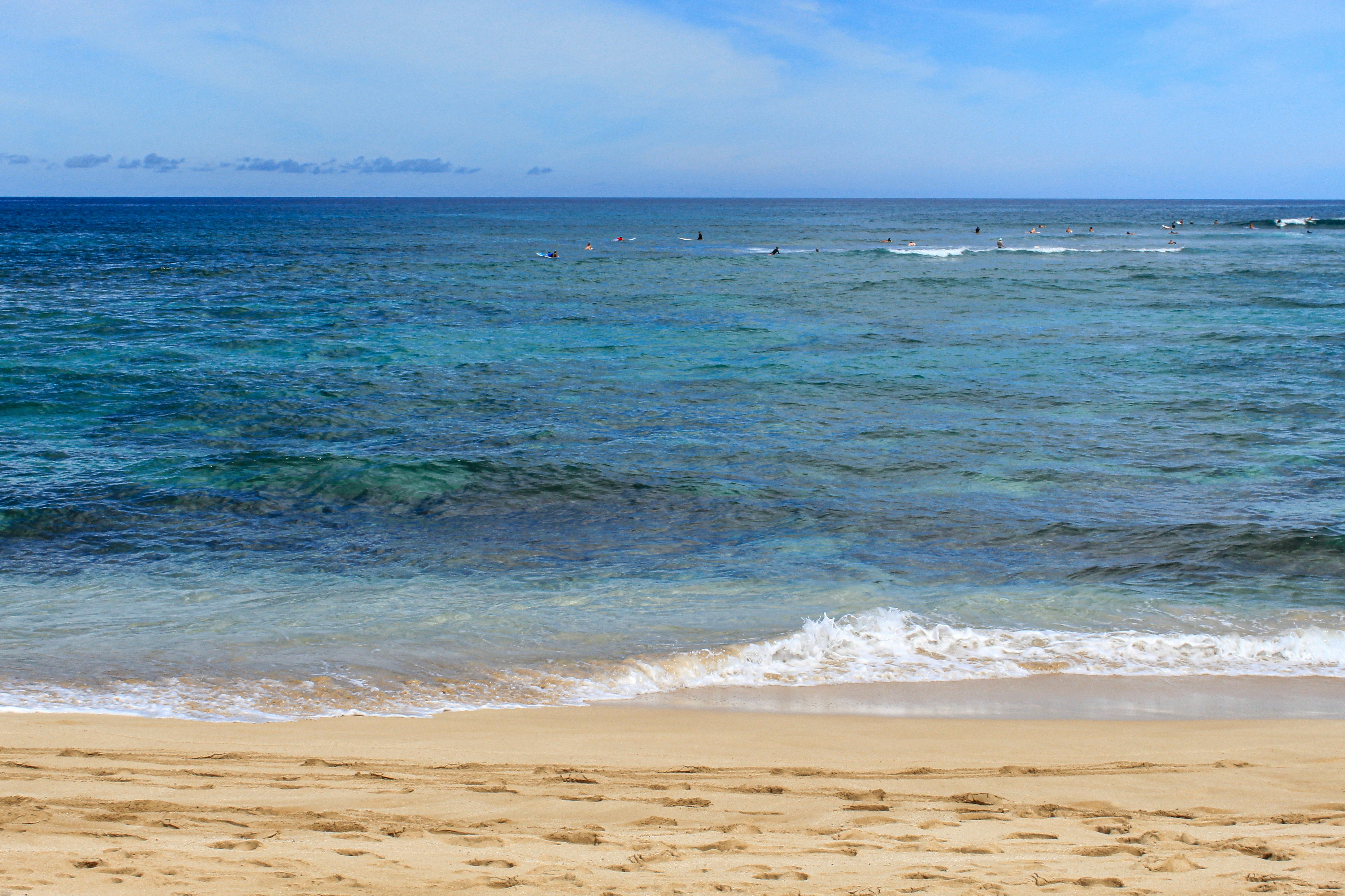 Gentle waves roll onto a sandy beach under a clear blue sky.