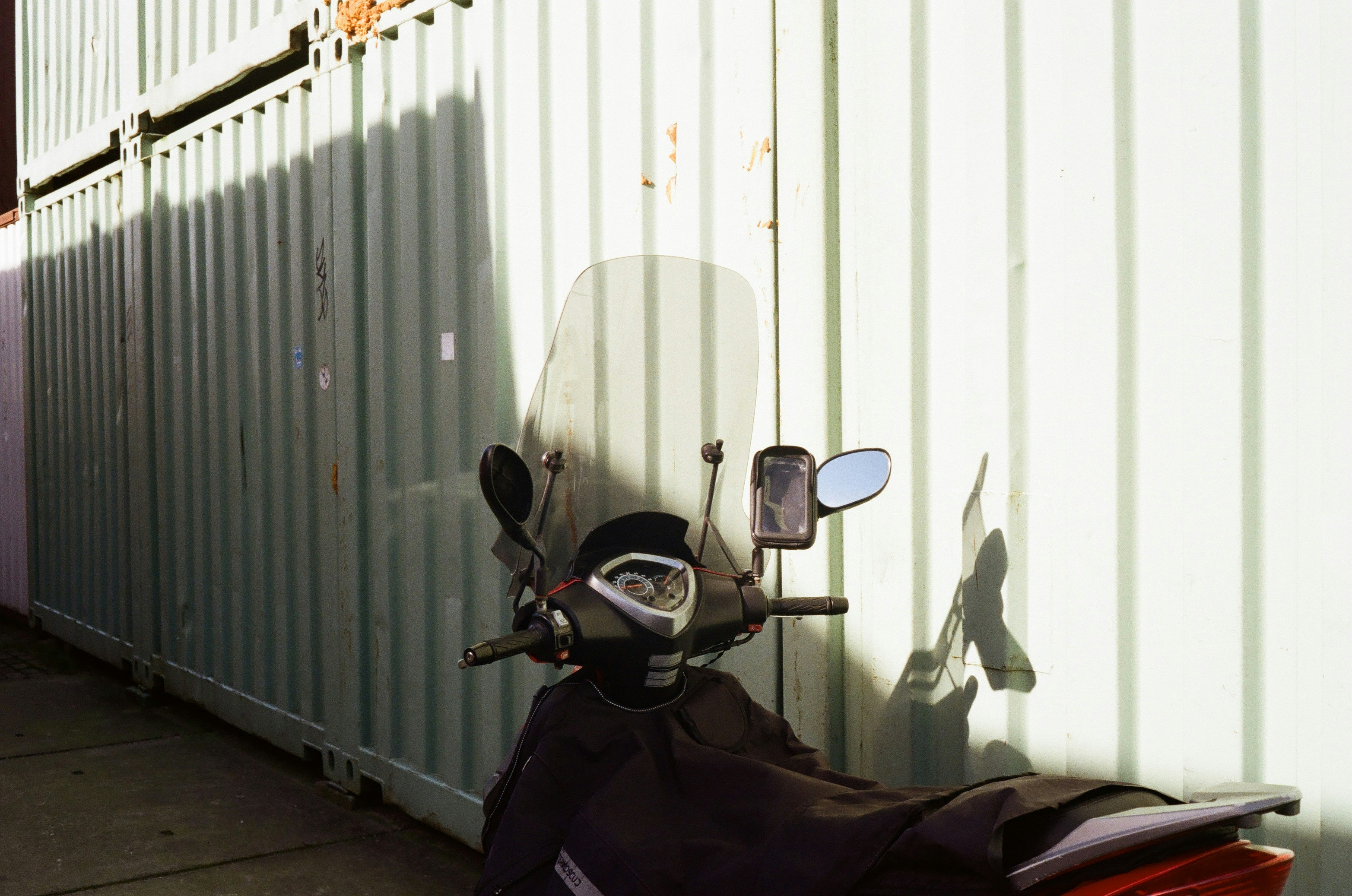 Motorbike casting a shadow on a sunlit shipping container wall.