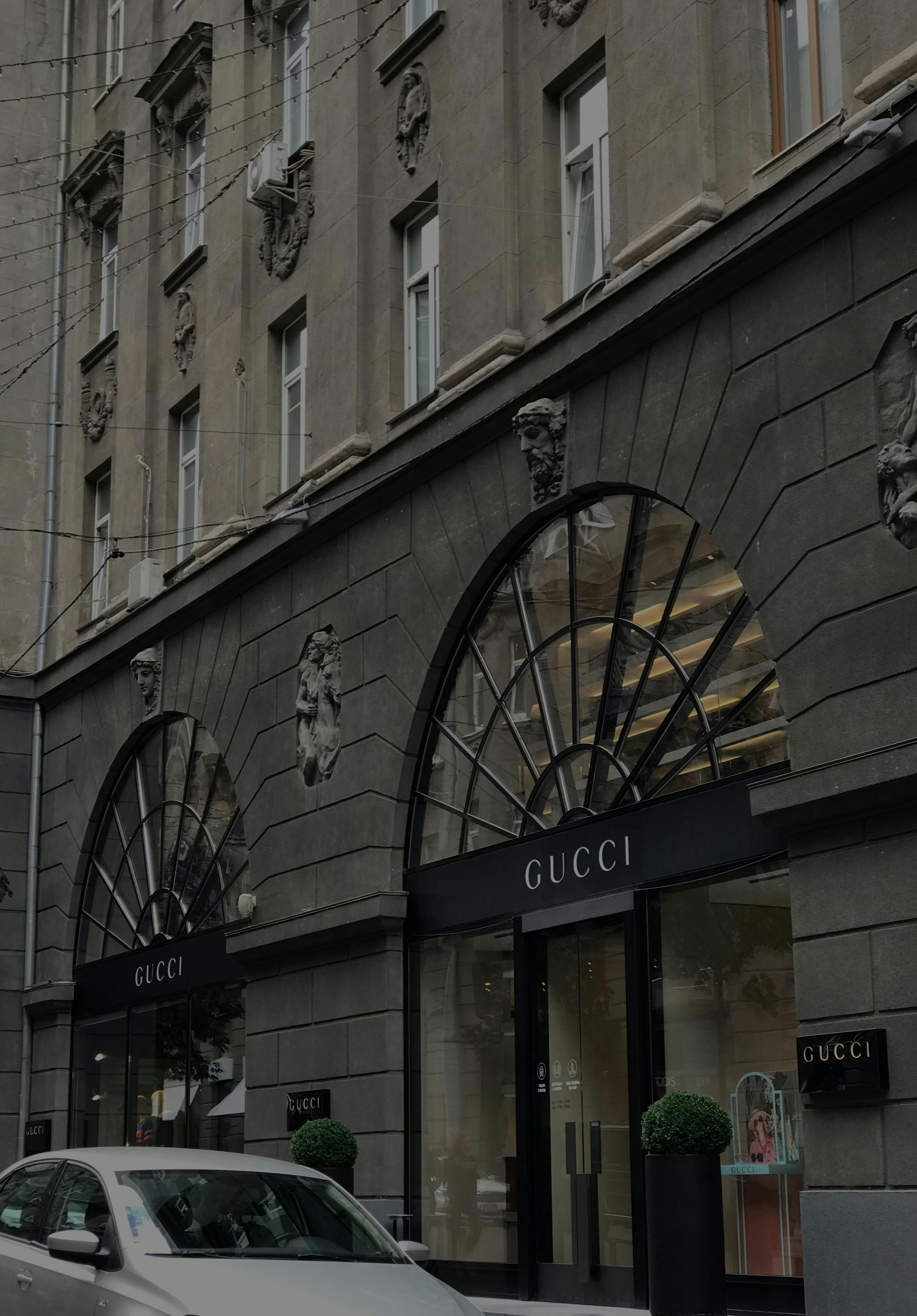 Gucci storefront featuring intricate architectural details and large arched windows, set against a muted urban backdrop.